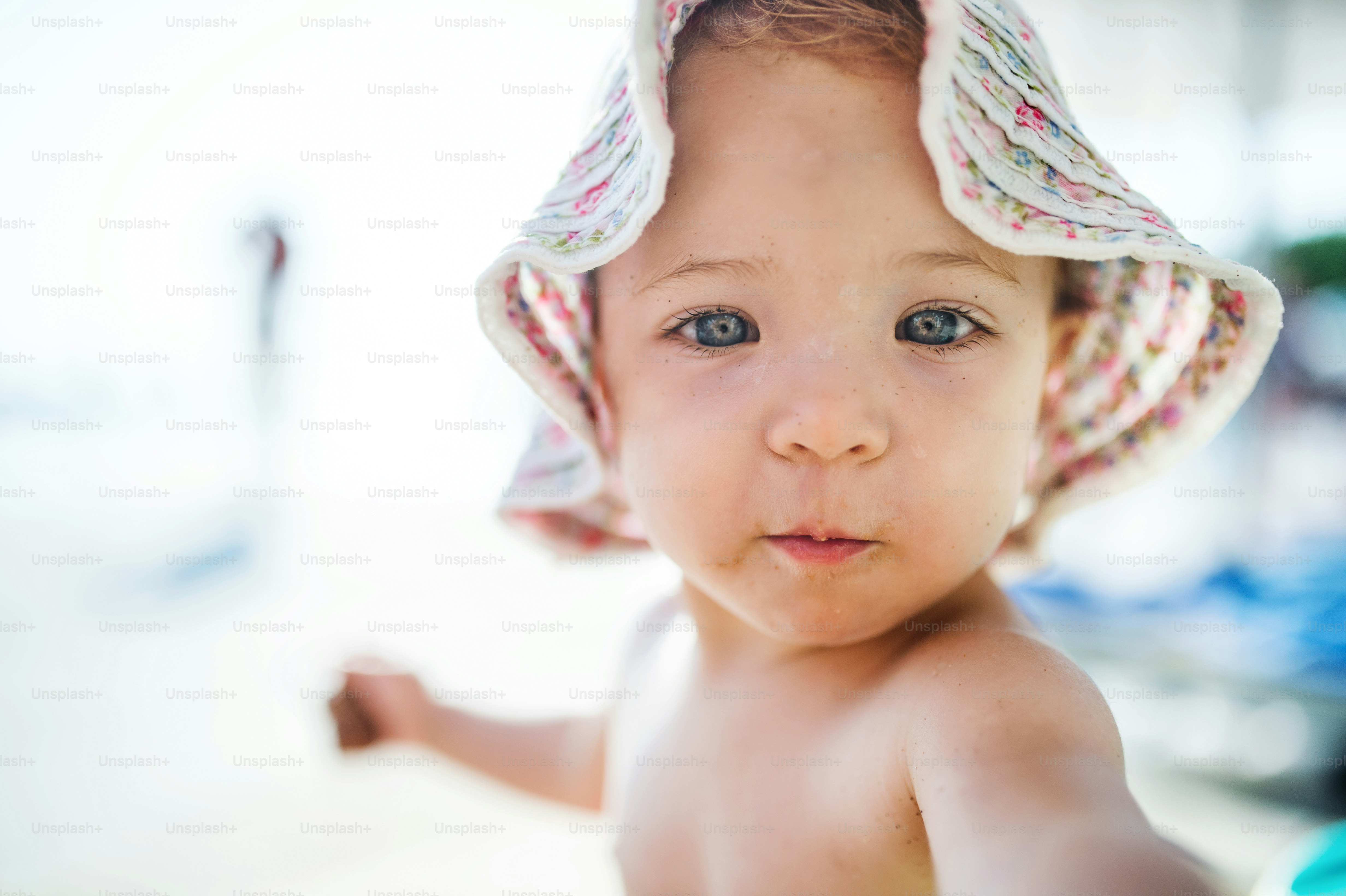 A close-up of cute small toddler girl sitting on beach on summer ...
