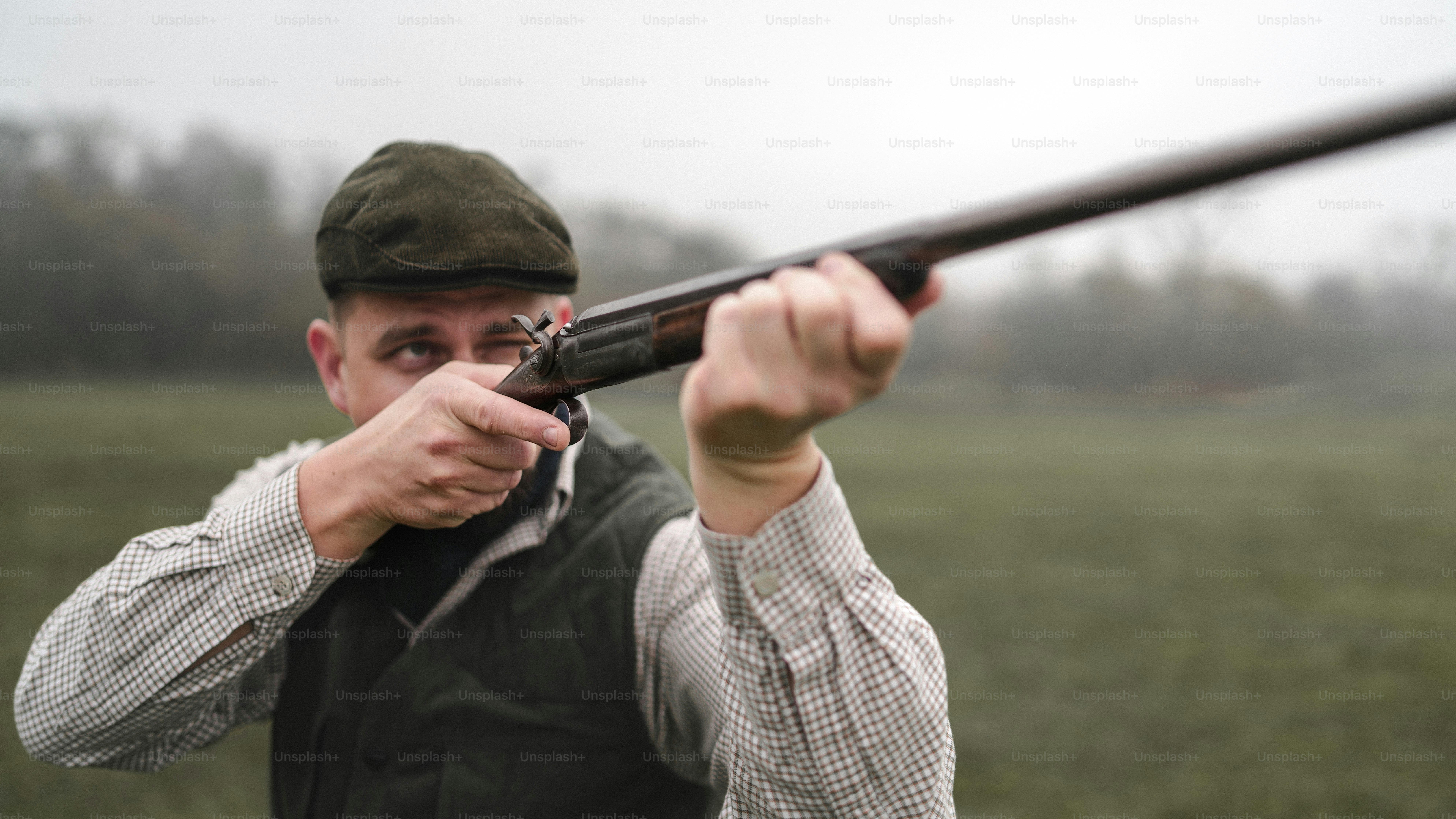A hunter man in traditional shooting clothes on field aiming with ...