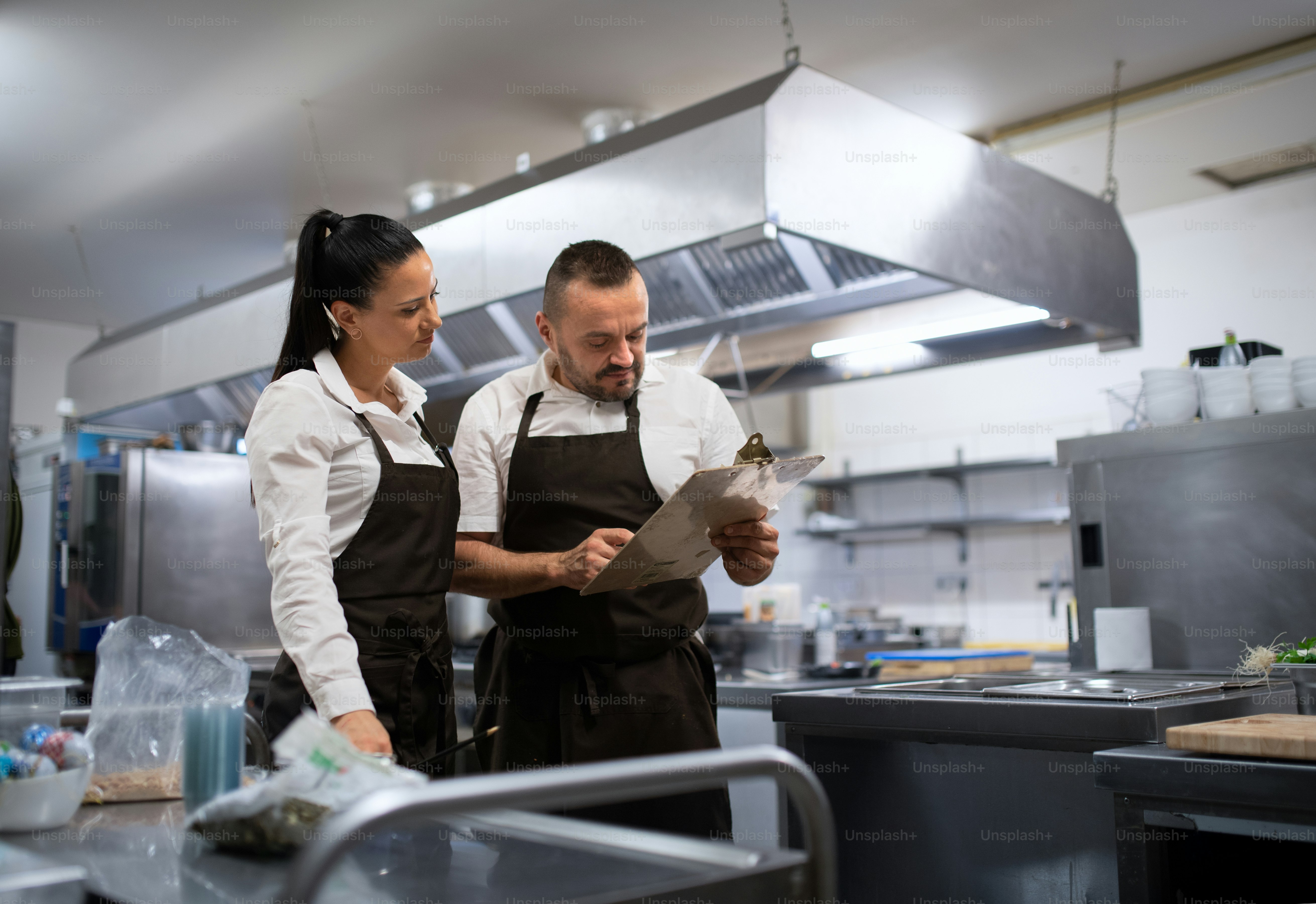 A chef and cook discussing menu indoors in restaurant kitchen. photo ...