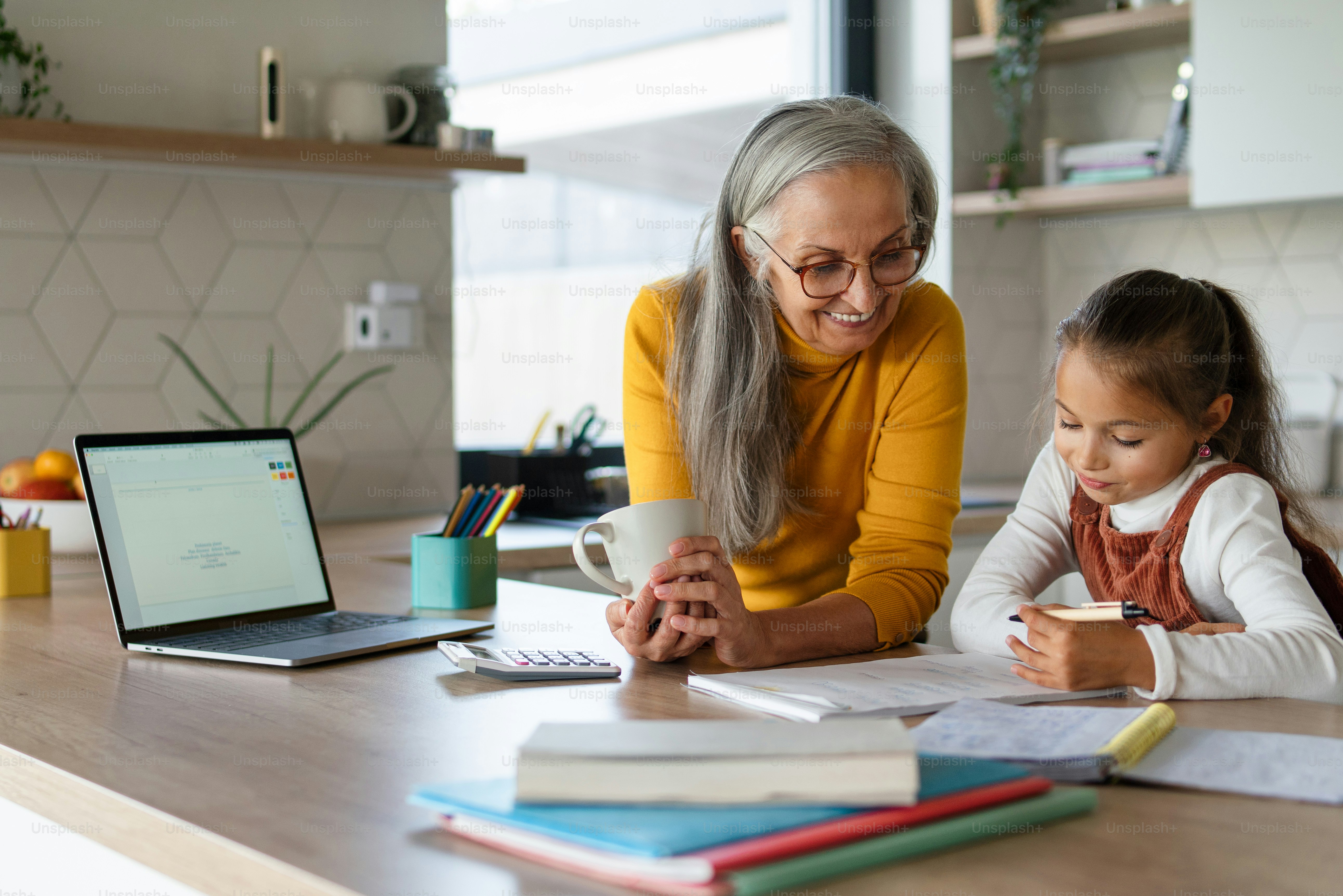 A small girl with senior grandmother doing homework at home.A small ...