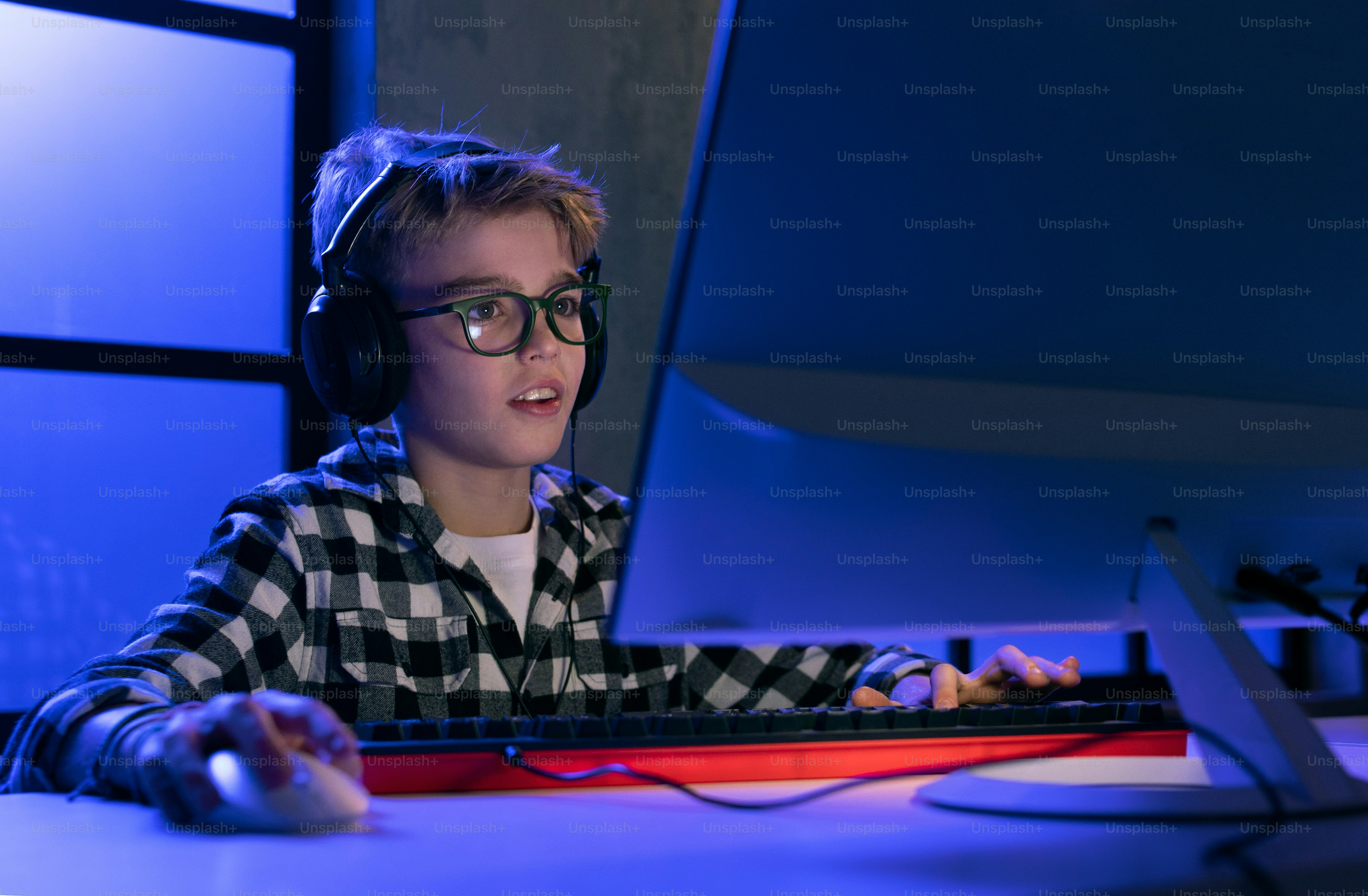 A young gamer boy with headphones playing computer video game. photo ...