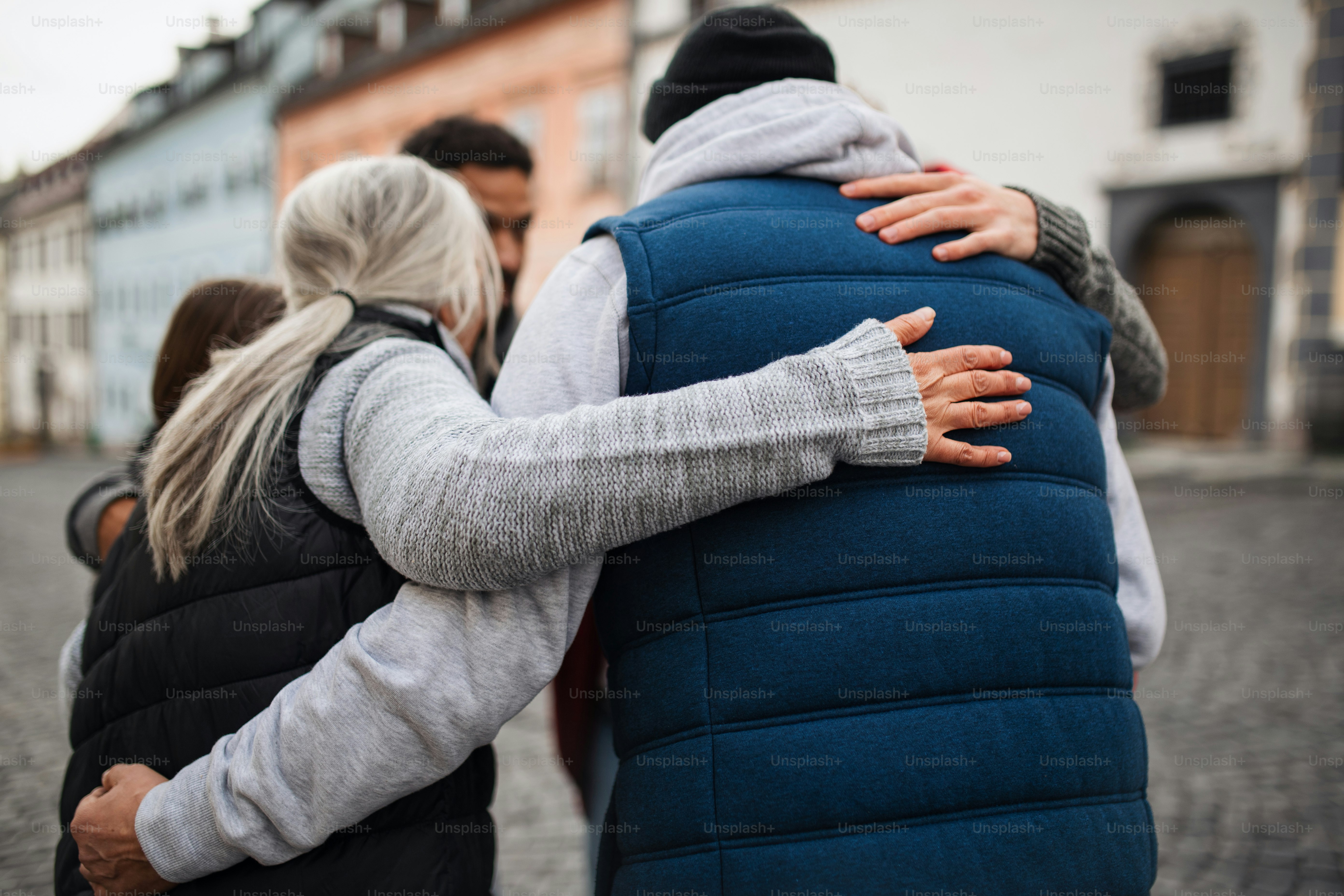 A rear view of community service volunteers hugging together outdoors ...