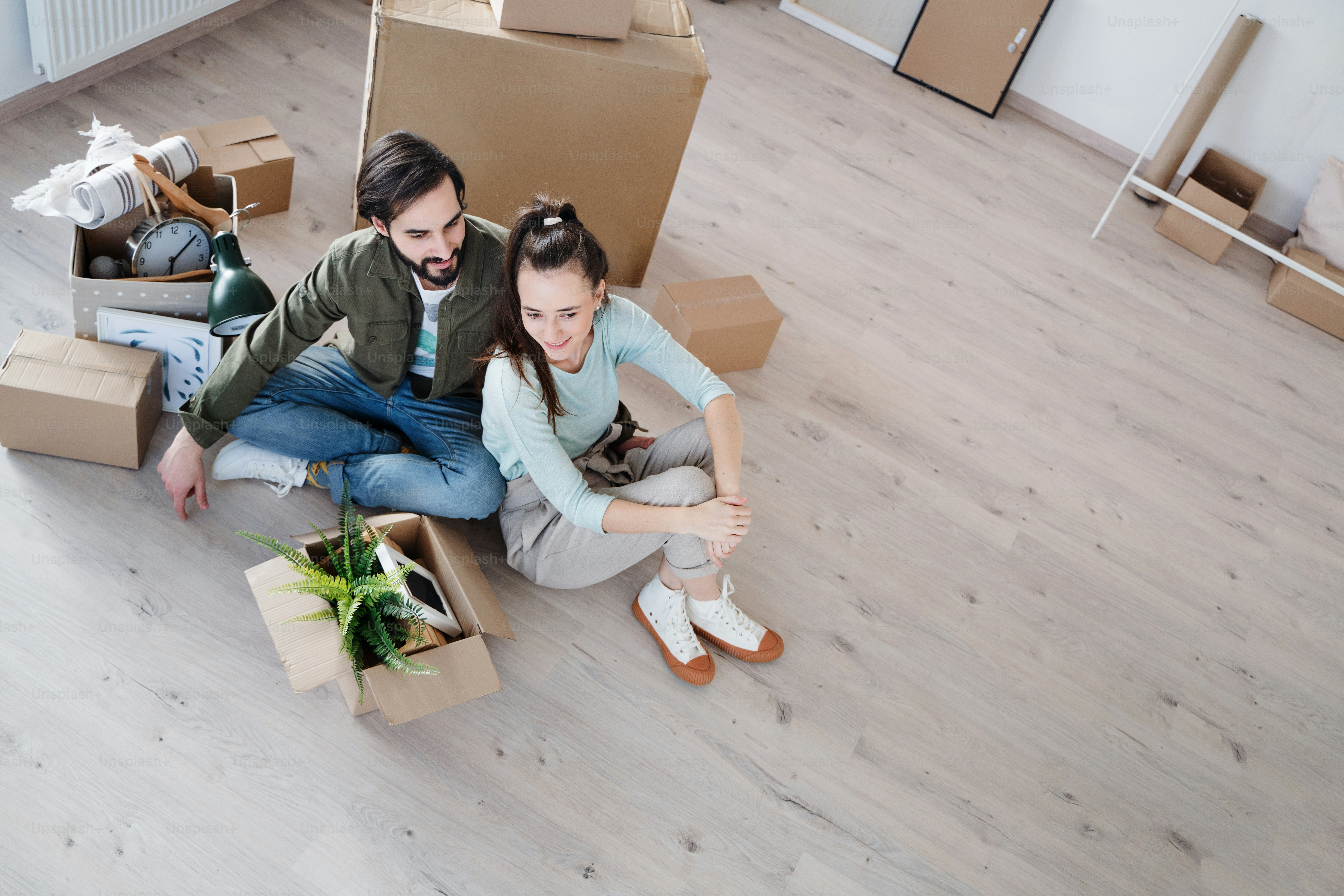 A high angle view of young couple with boxes sitting on floor when moving in new flat, new home ...