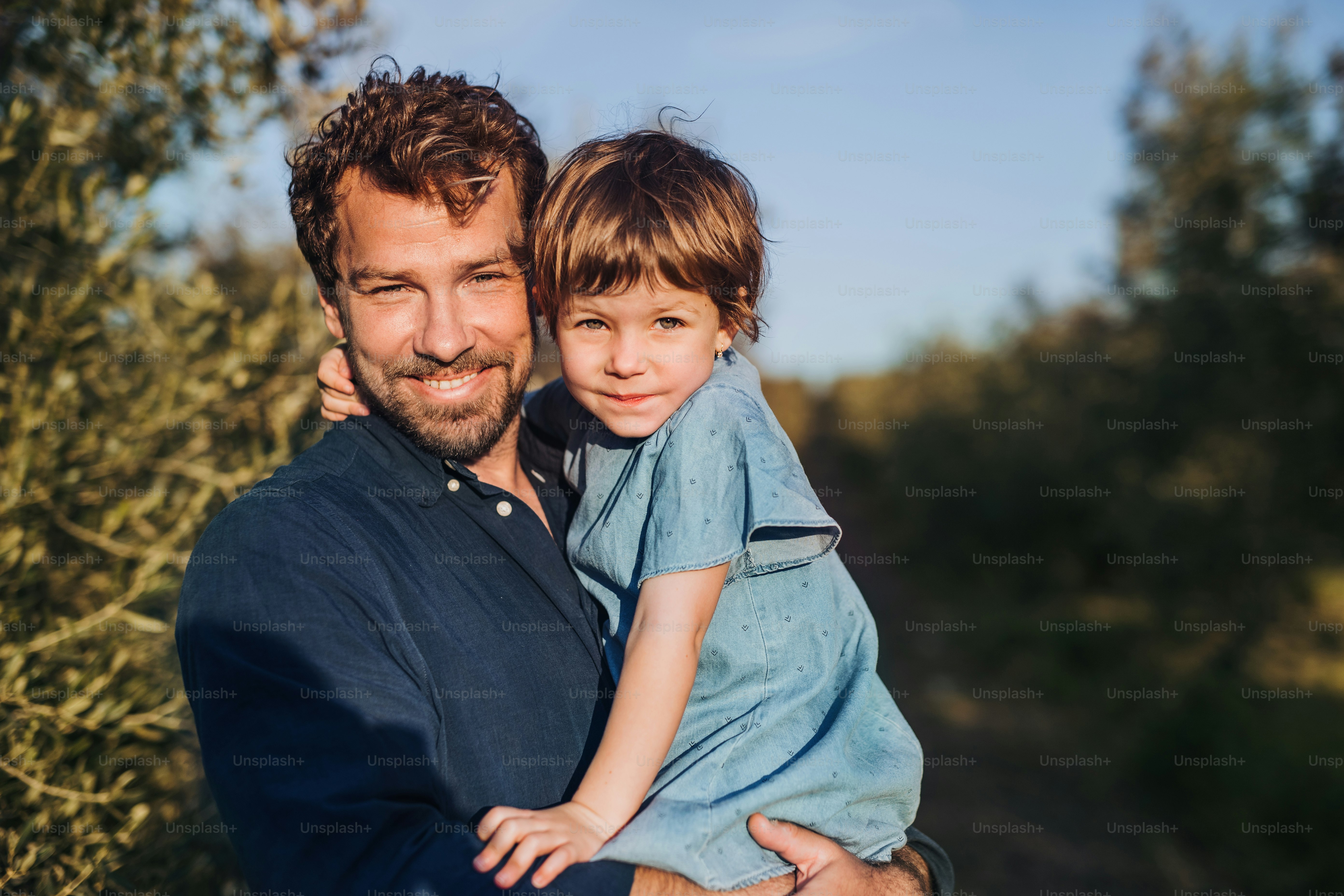 Portrait of father holding small daughter standing outdoors by olive ...