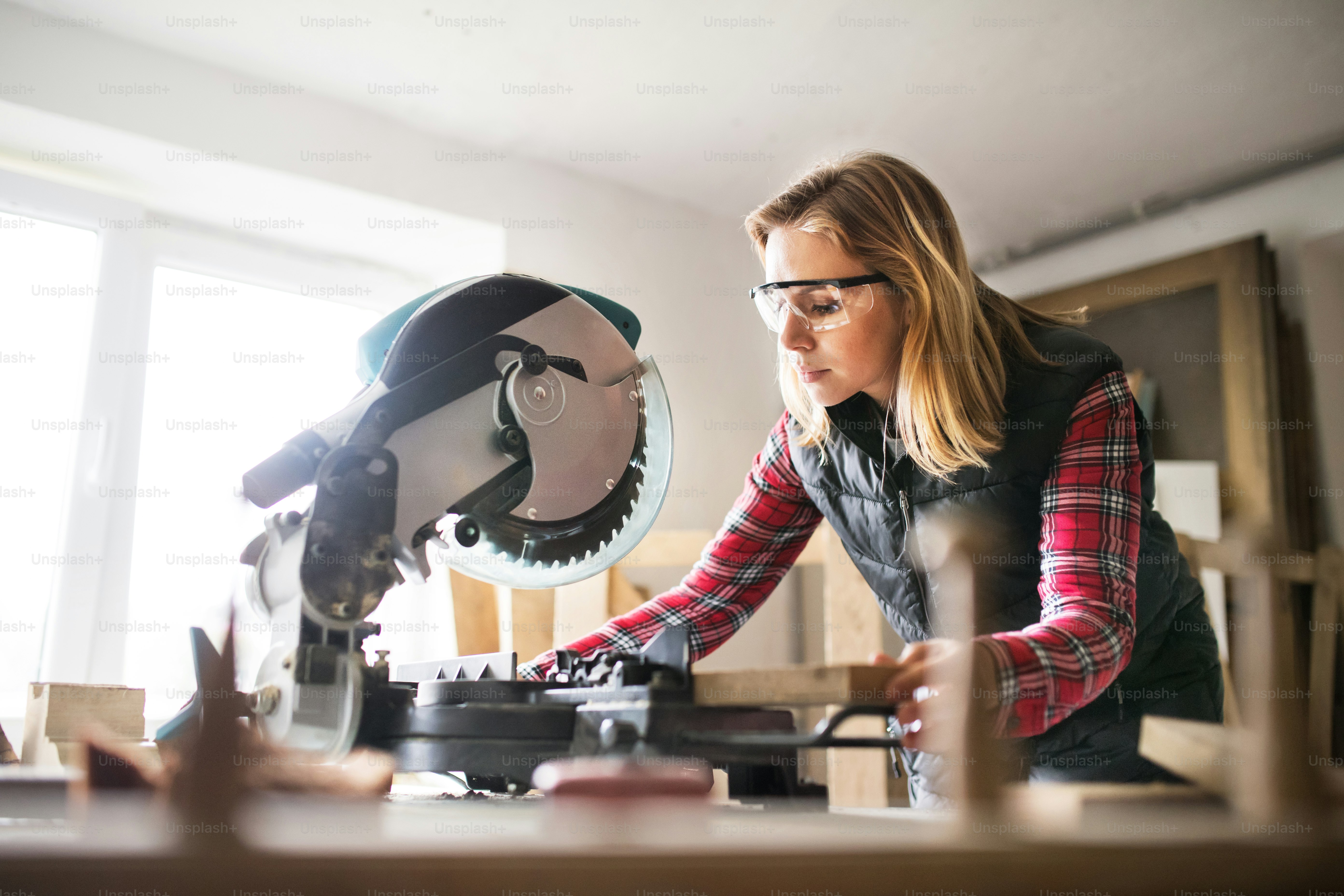 Young woman worker in workroom. Female carpenter using miter saw. photo ...