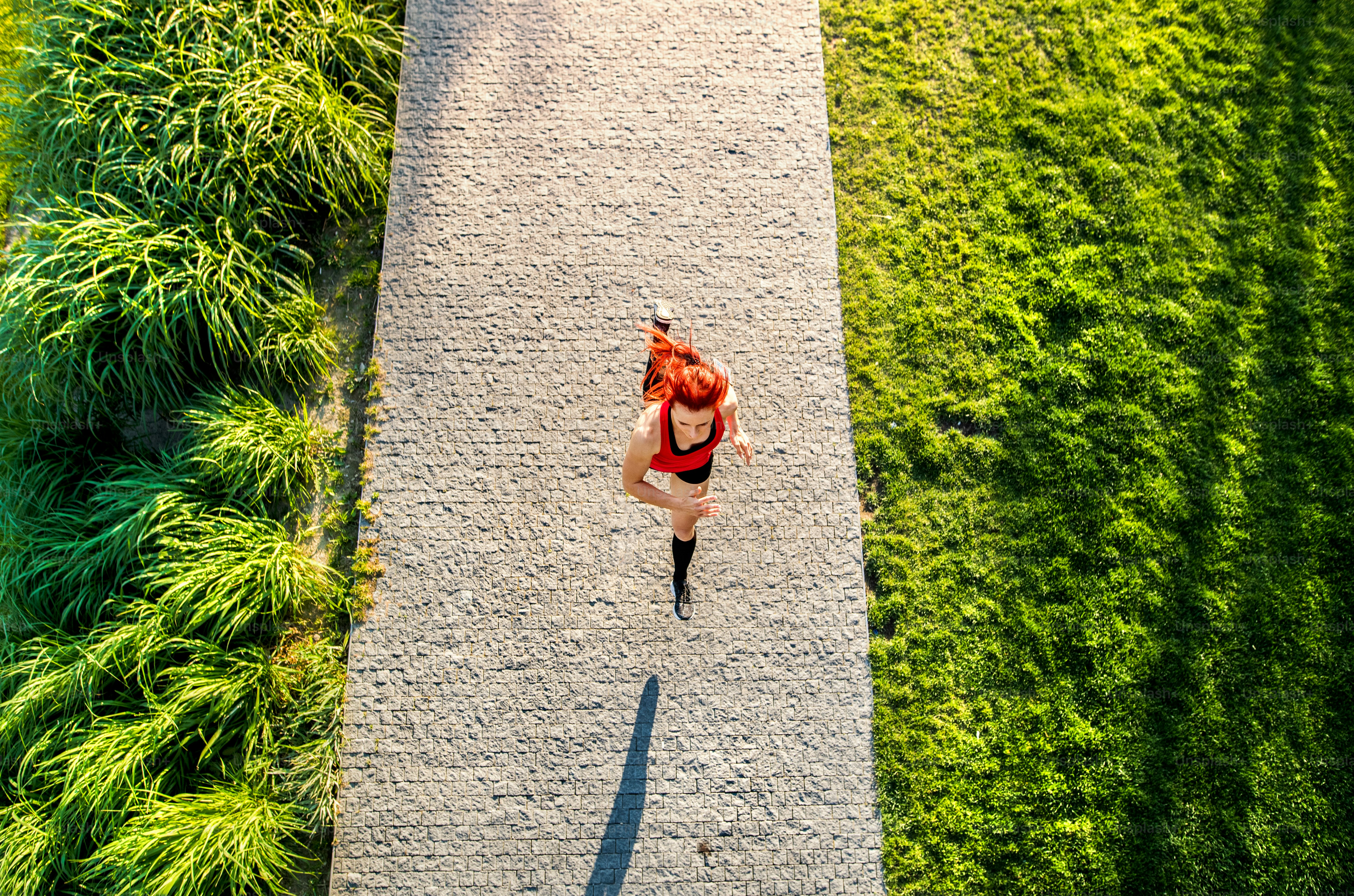 Beautiful young athlete in sports clothes running on concrete path in ...