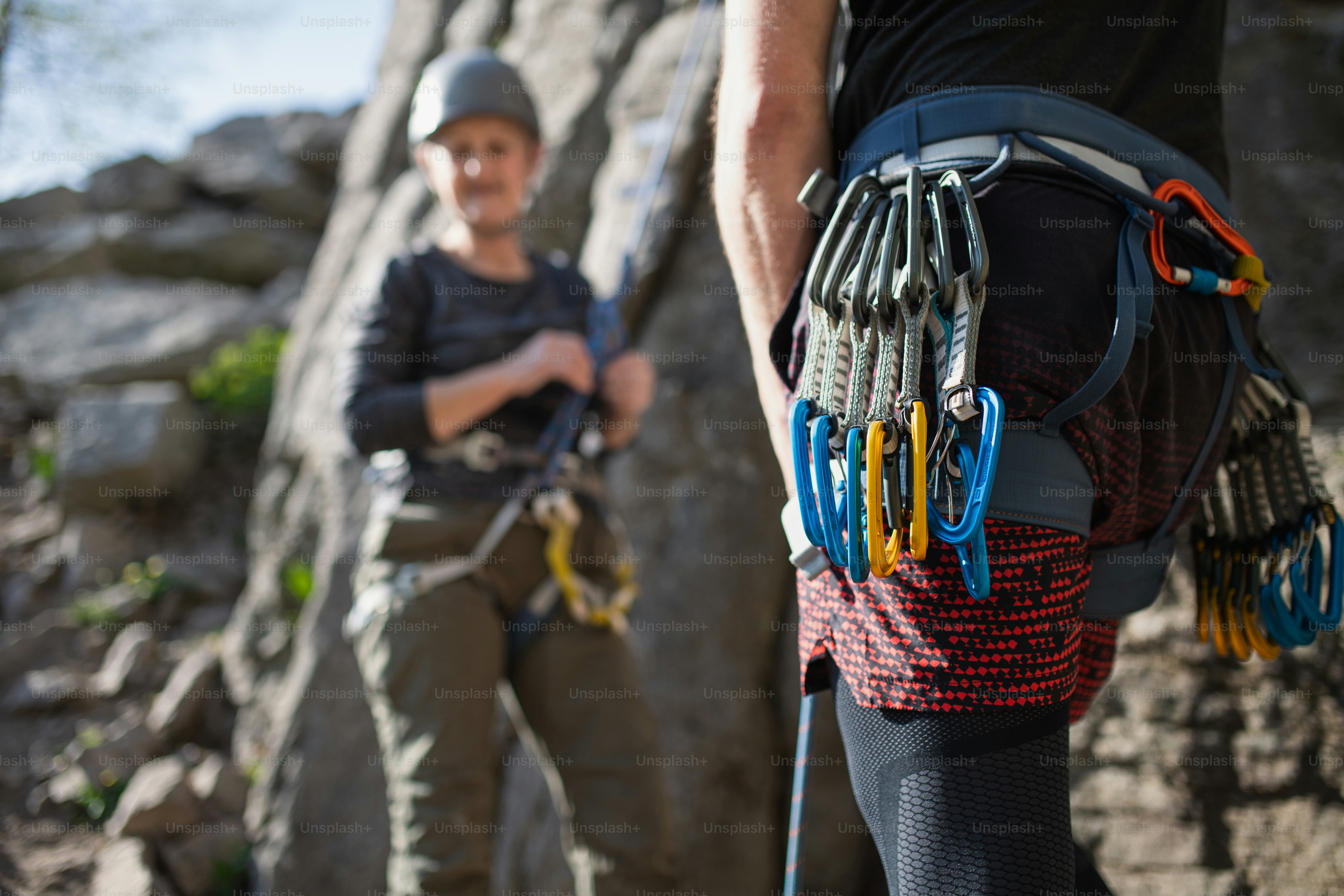 An unrecognizable instructor with harness and carabiners climbing rocks ...