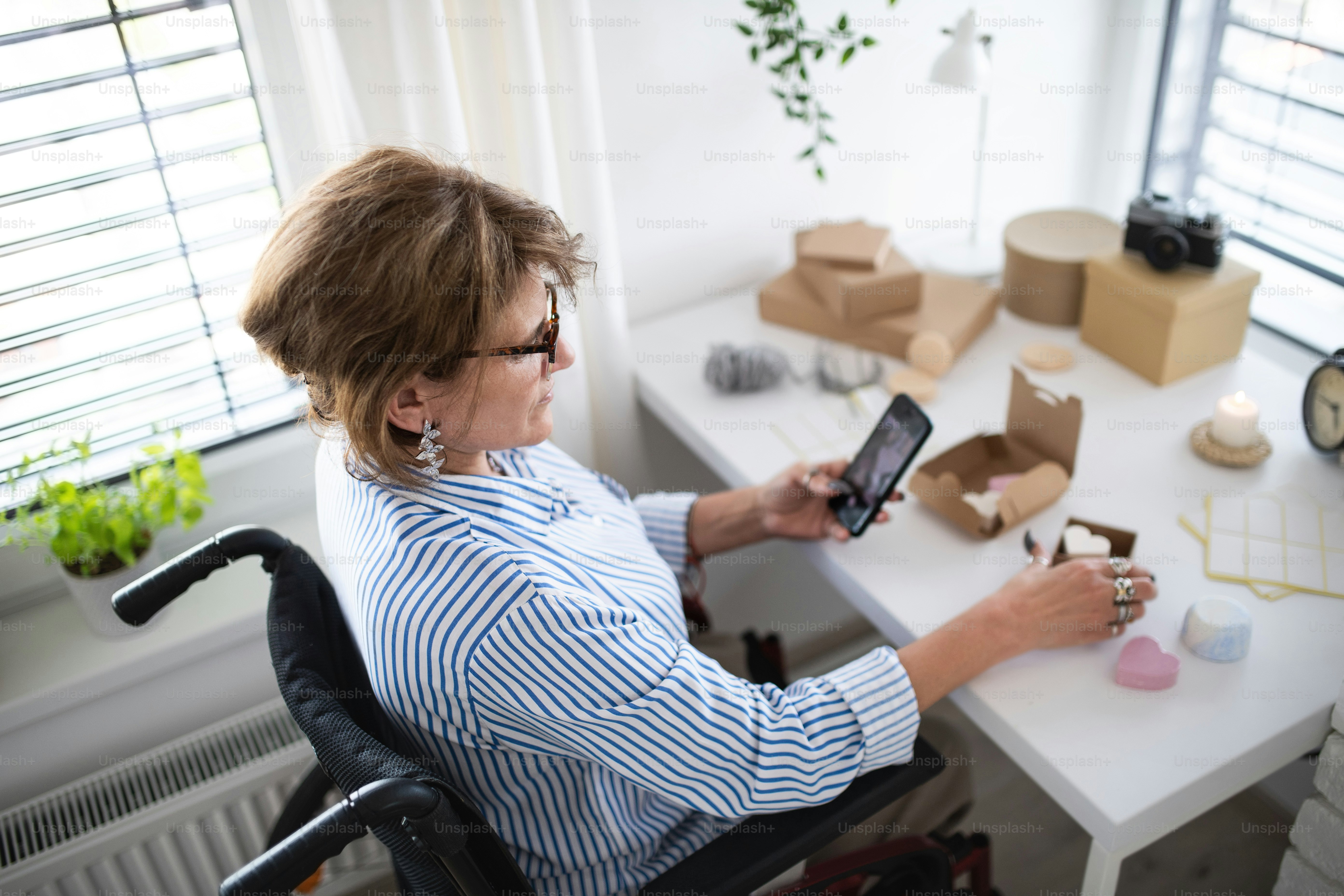 A disabled mature woman in wheelchair packing handmade products indoors ...