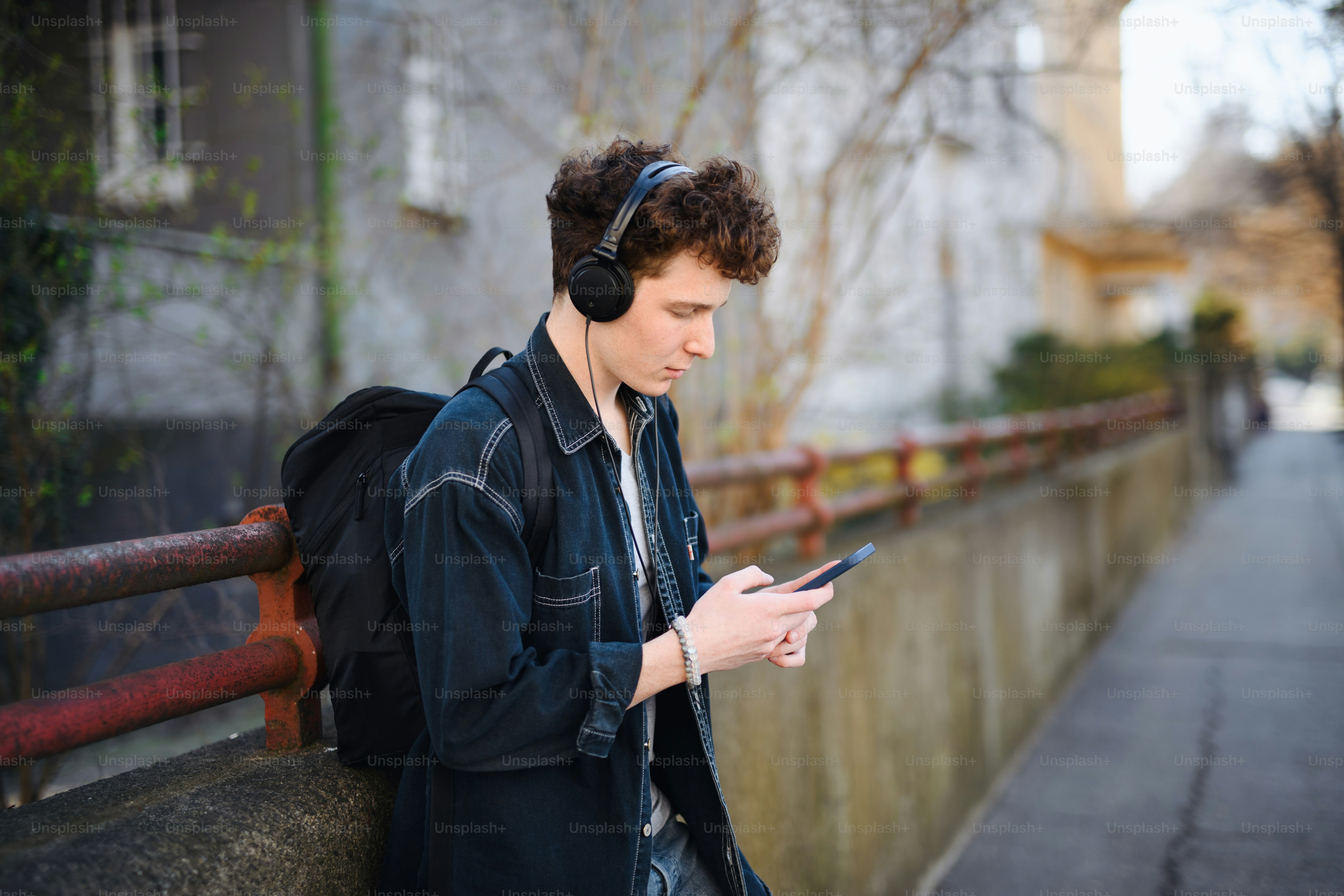 A portrait of young man commuter with headphones standing outdoors in ...