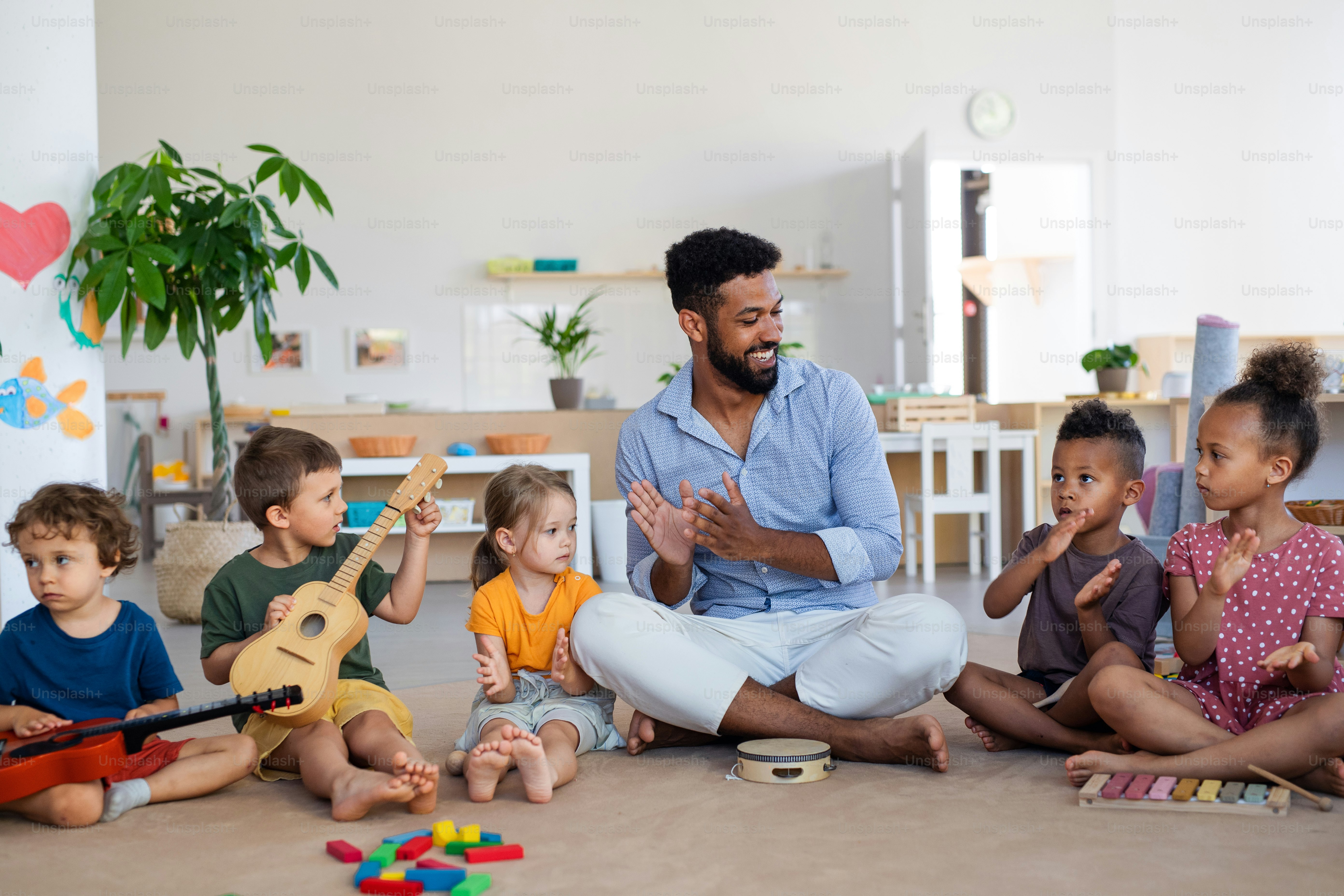 A group of small nursery school children with man teacher sitting on ...