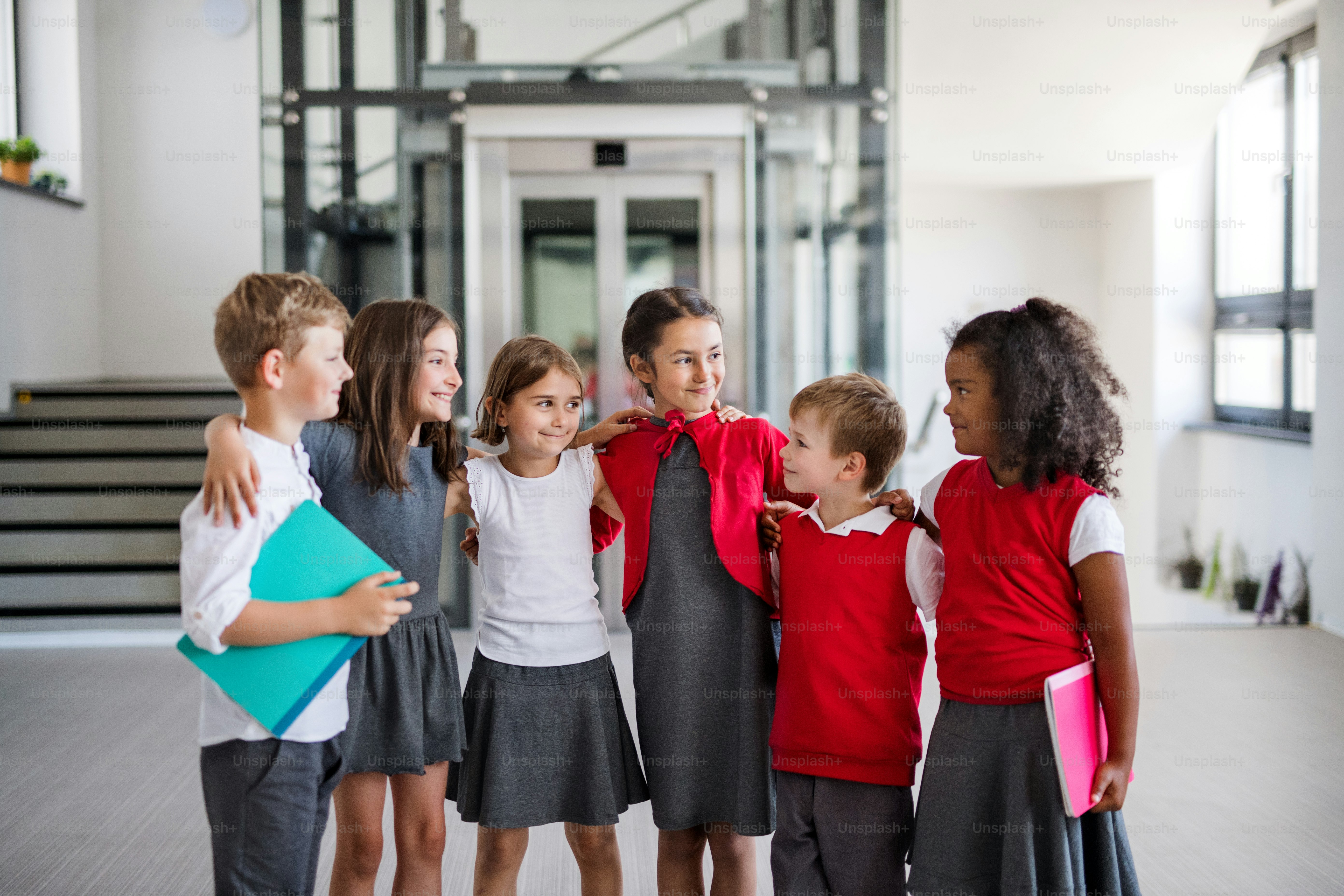 A group of cheerful small school kids in corridor, running and jumping ...