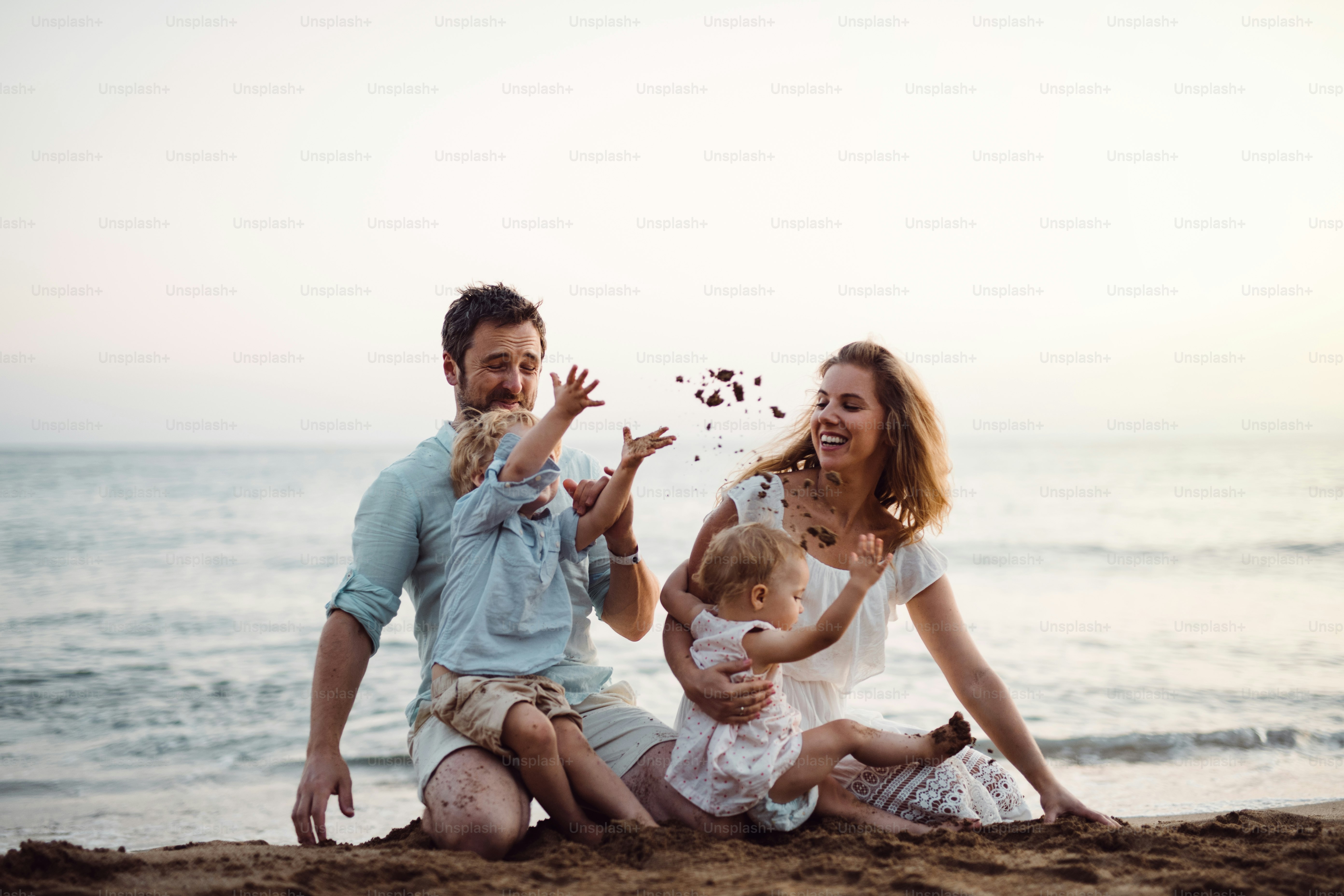 A family with two toddler children sitting on sand beach on summer ...