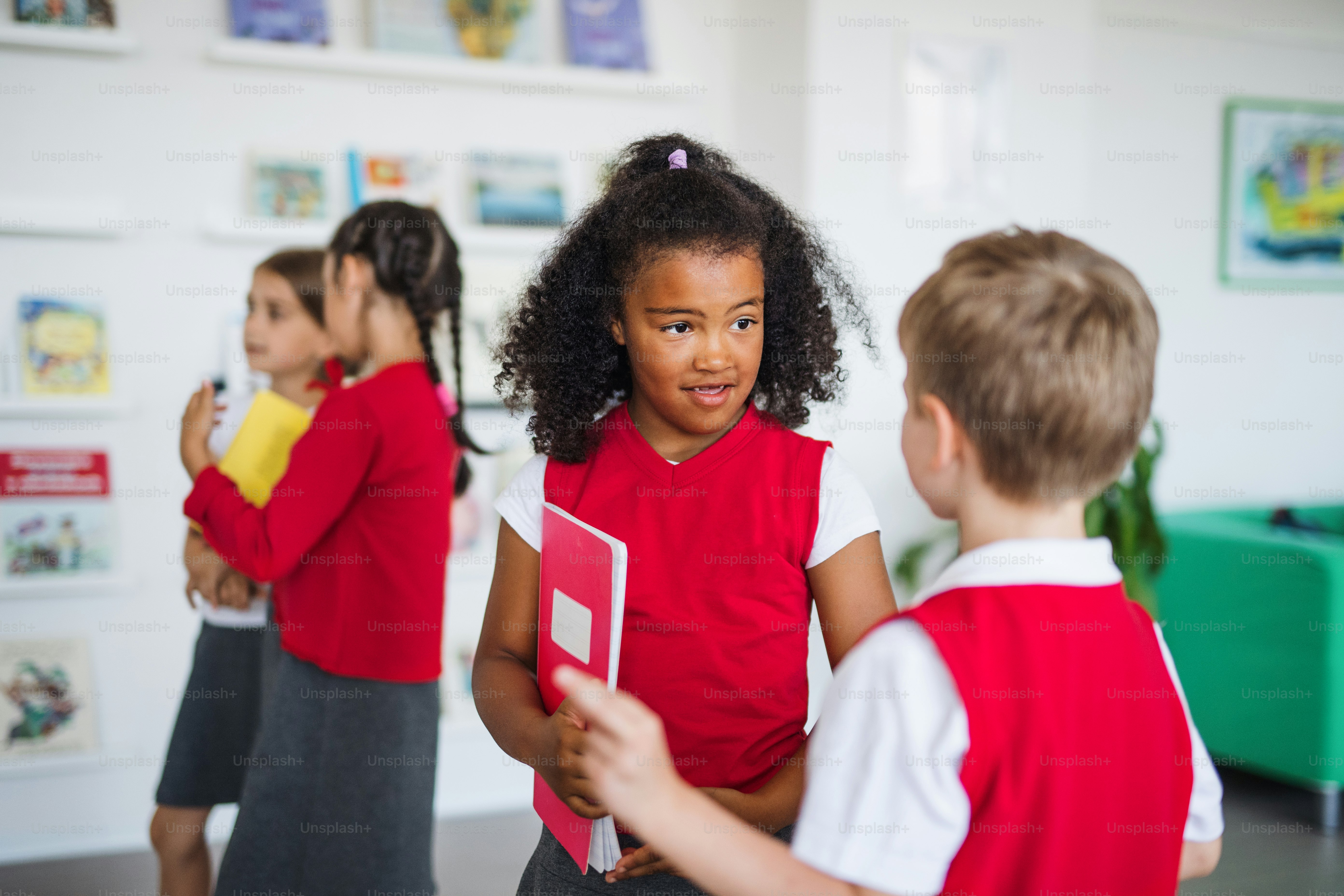 A group of cheerful small school kids in corridor, standing and talking ...