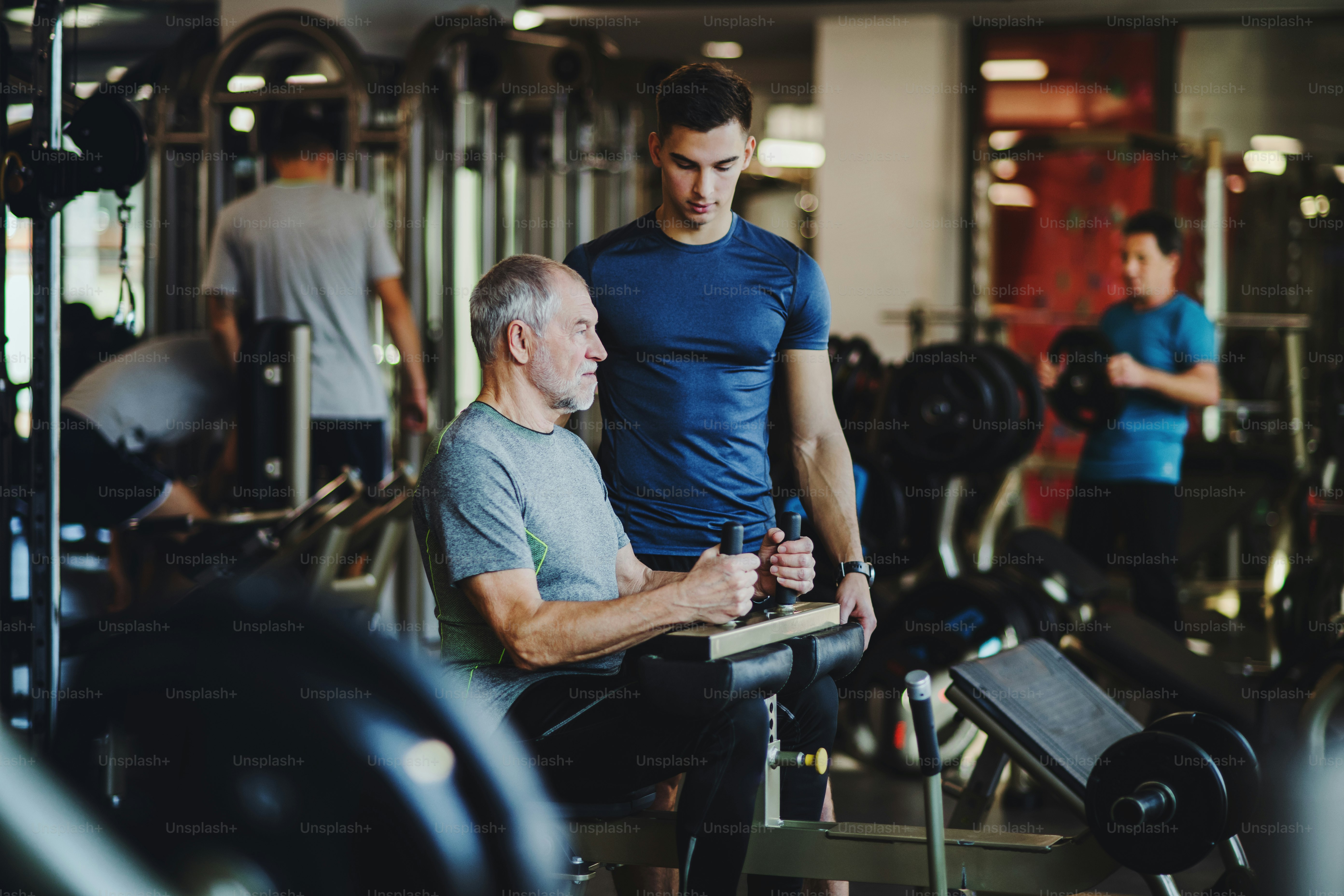 A senior man with a young male trainer doing strength workout exercise ...
