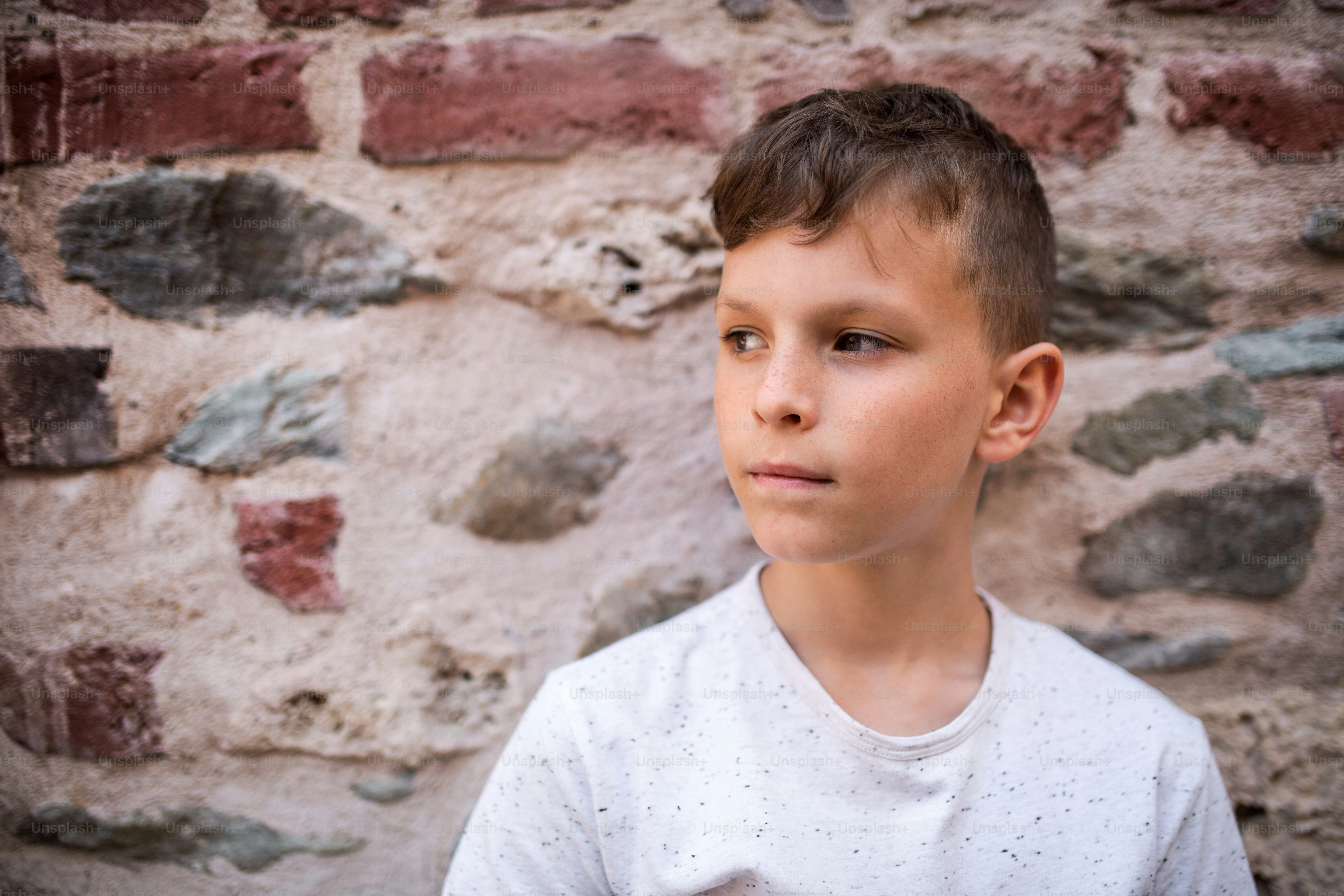 A portrait of small boy standing outdoors in front of old brick wall ...
