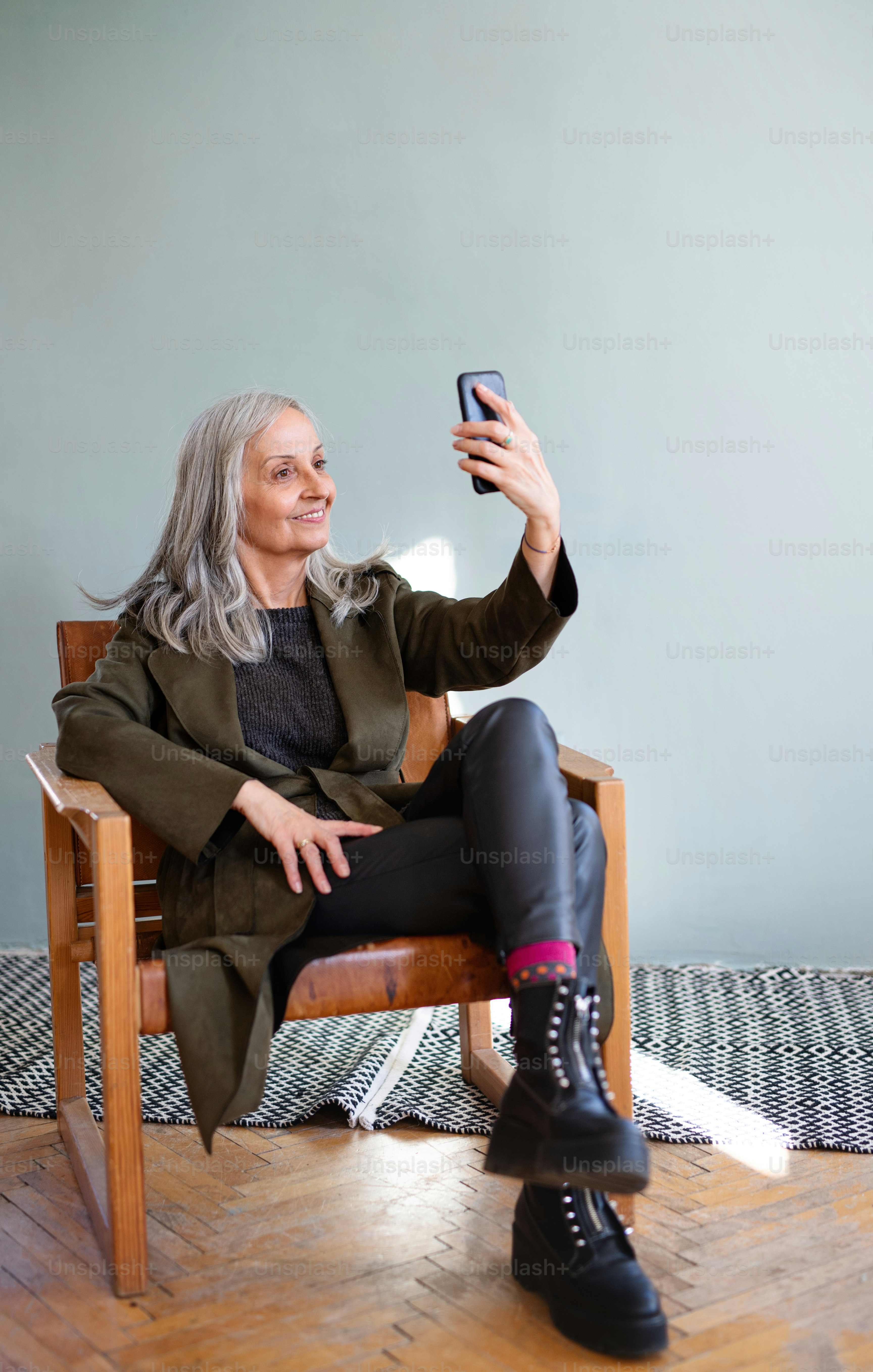 Portrait of senior woman with sitting indoors on chair, taking selfie ...