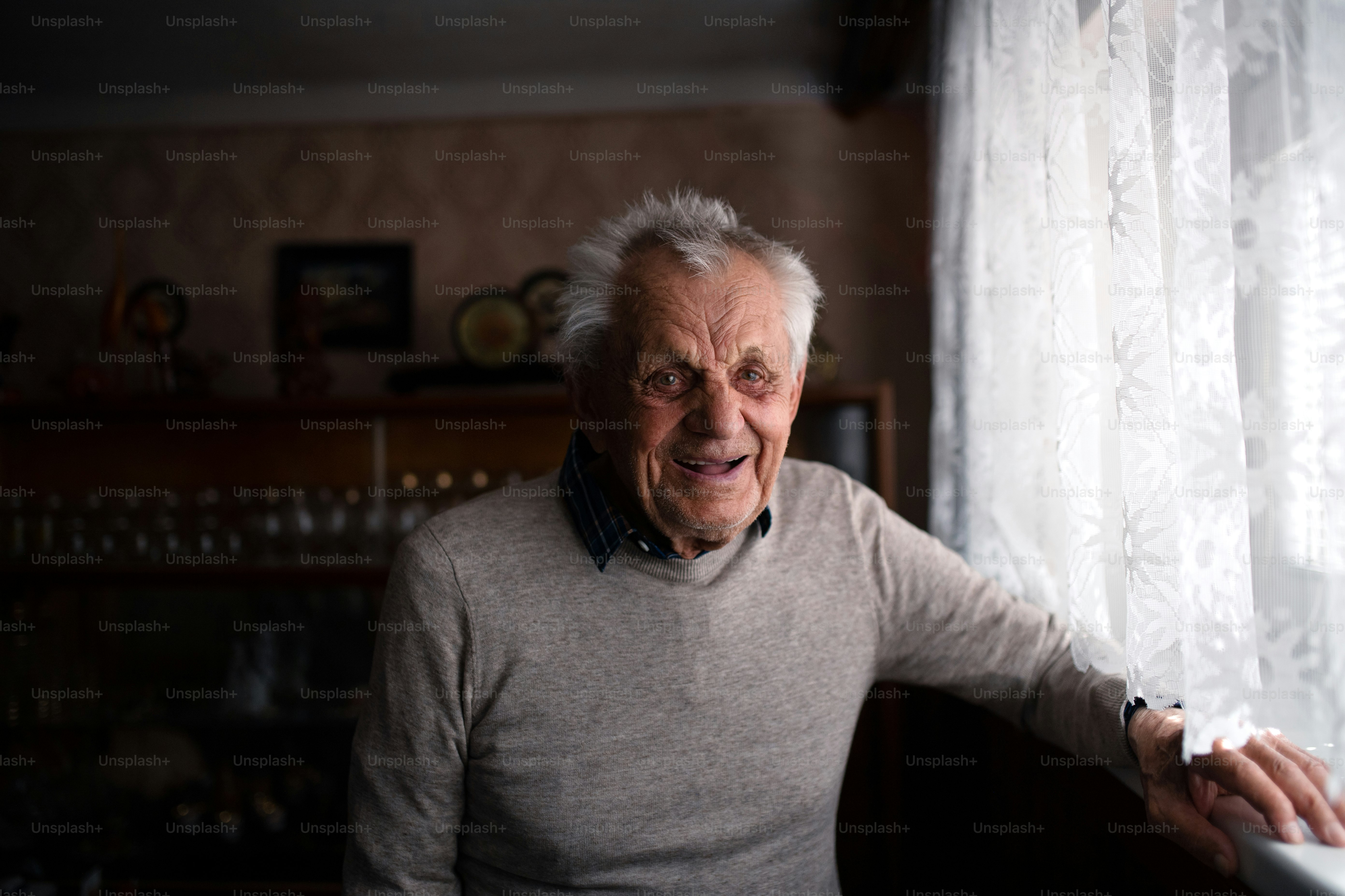 A portrait of elderly man standing indoors at home, looking at camera ...