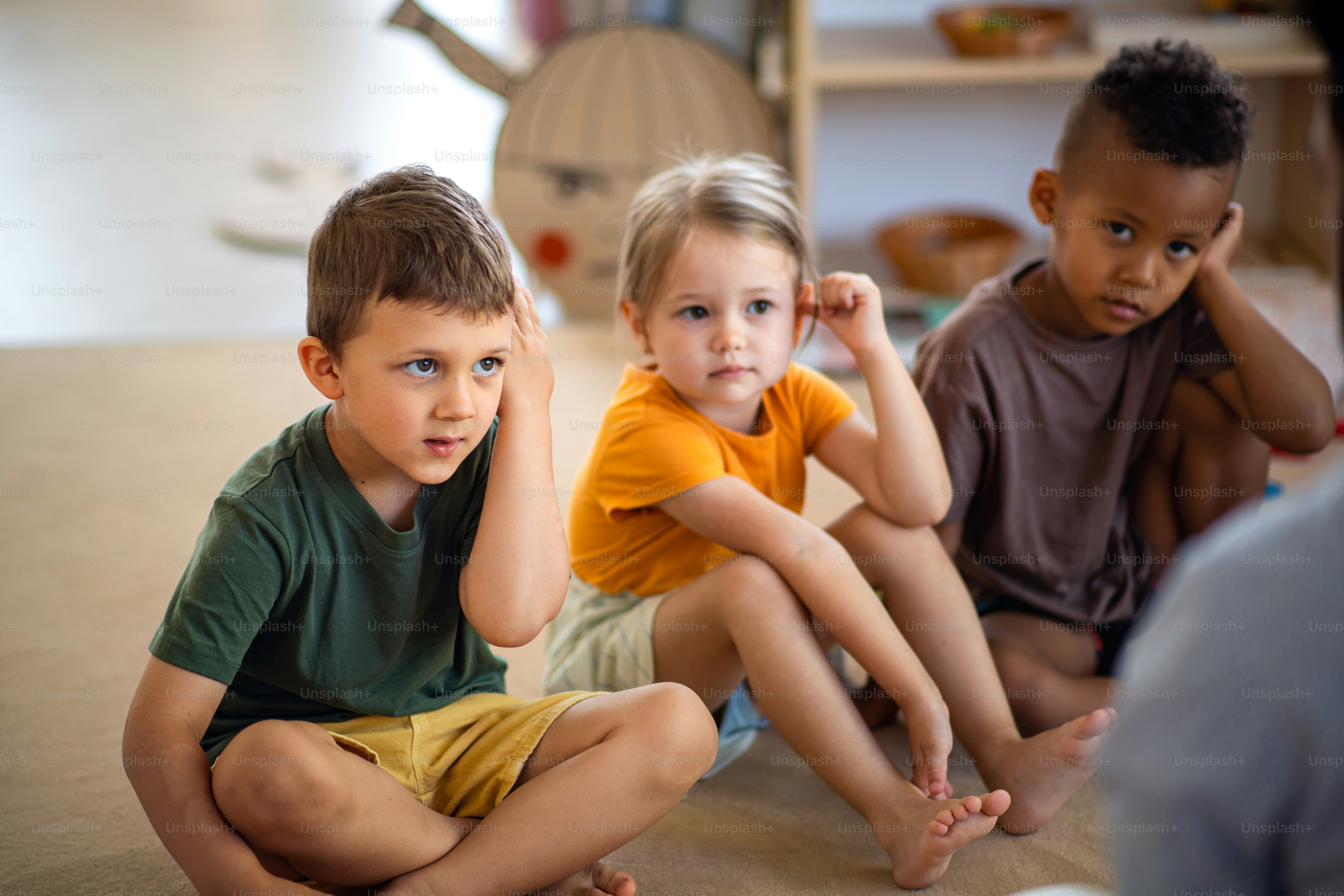 A group of small nursery school children sitting on floor indoors in ...