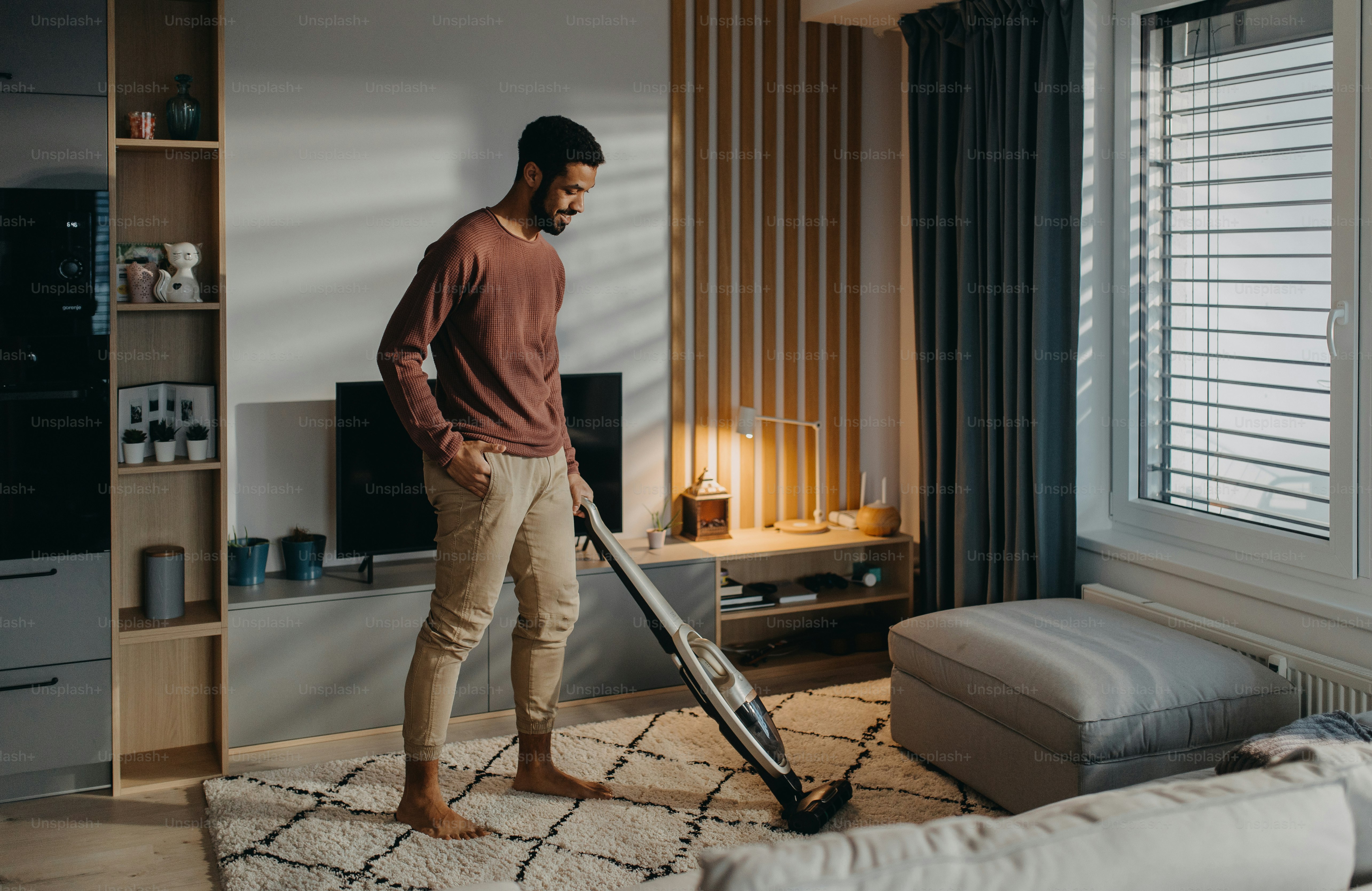 A young man hoovering carpet with vacuum cleaner in living room photo ...