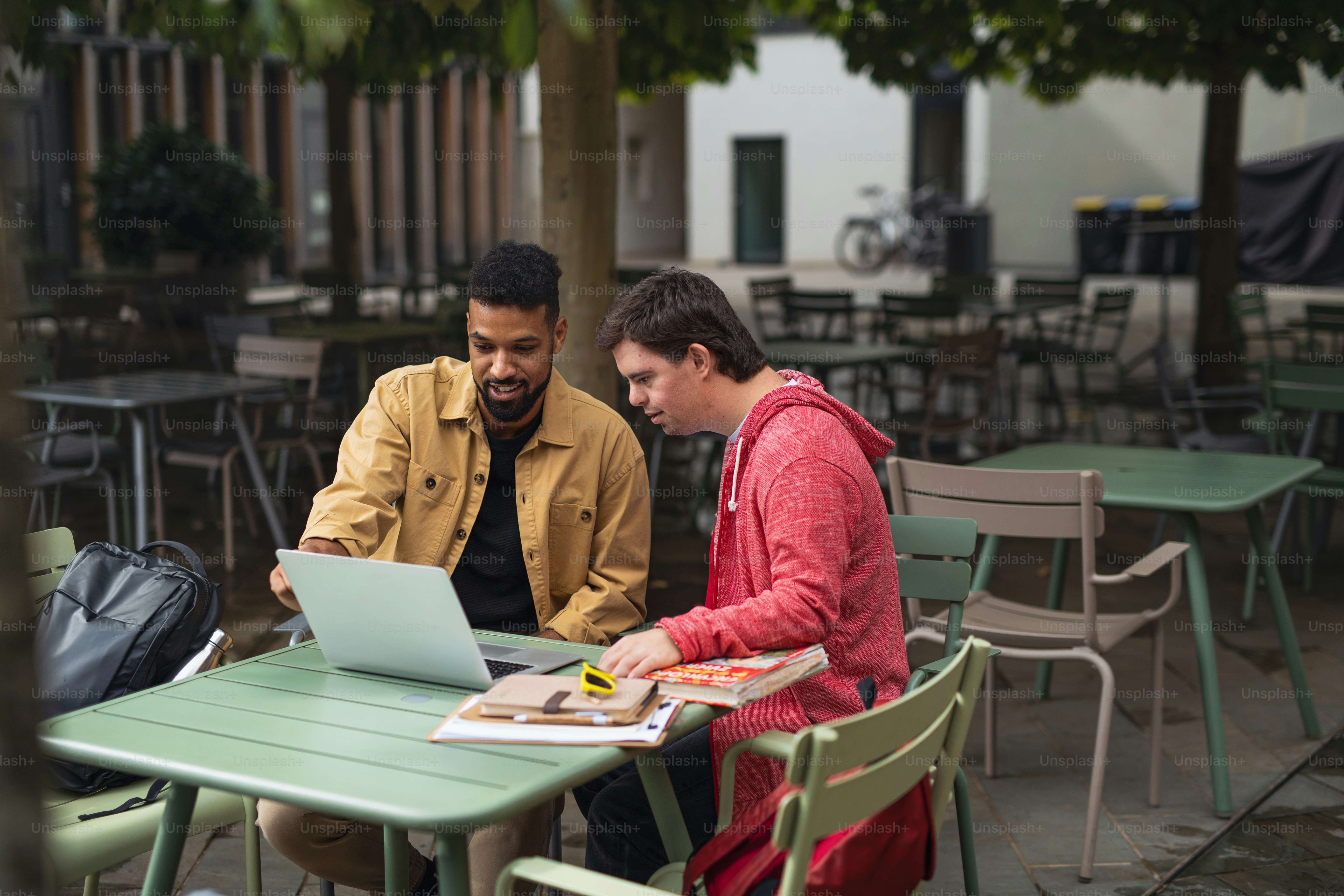A young man with Down syndrome with his mentoring friend sitting ...