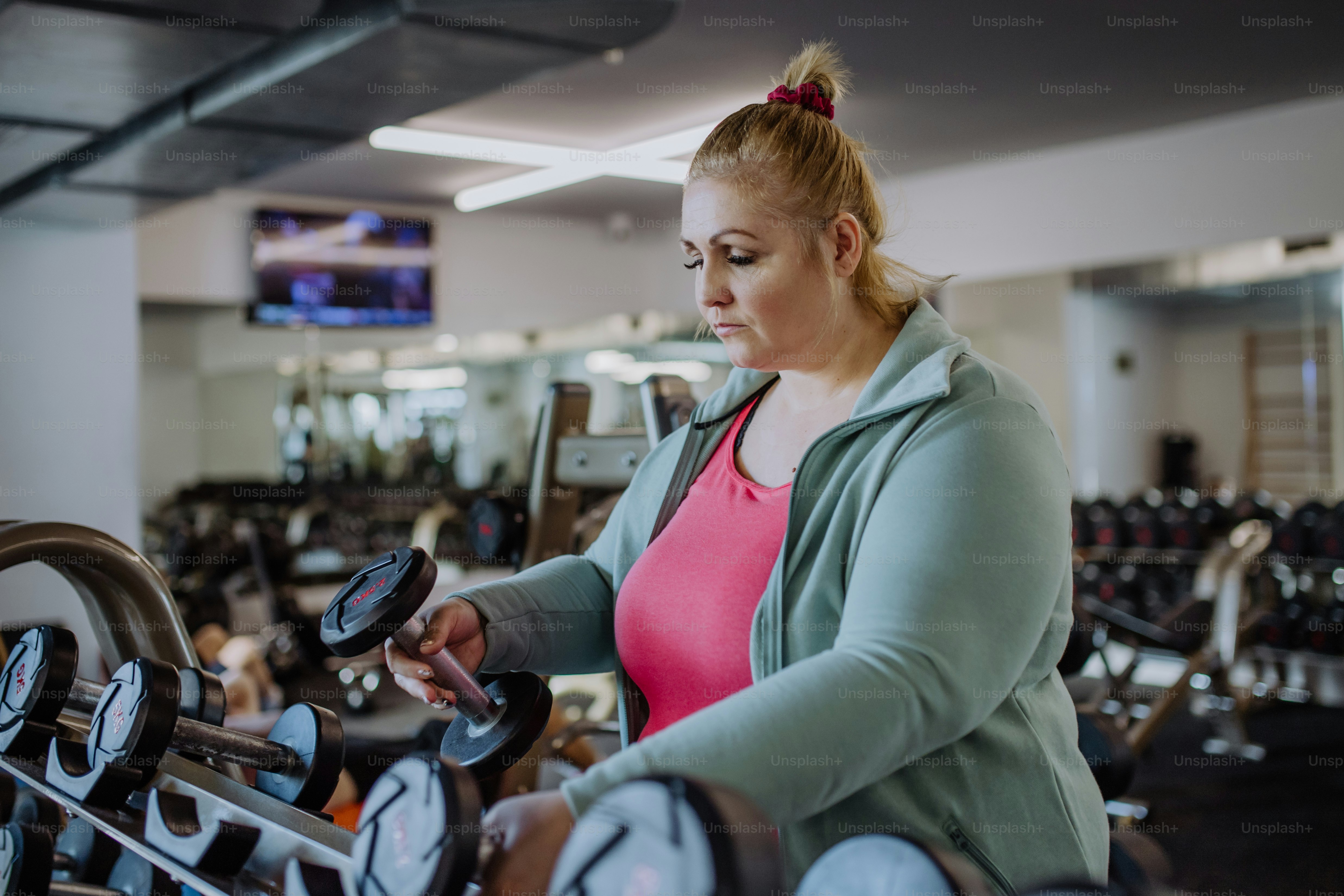 A plus size woman training taking dumbbells indoors in gym photo – Plus ...