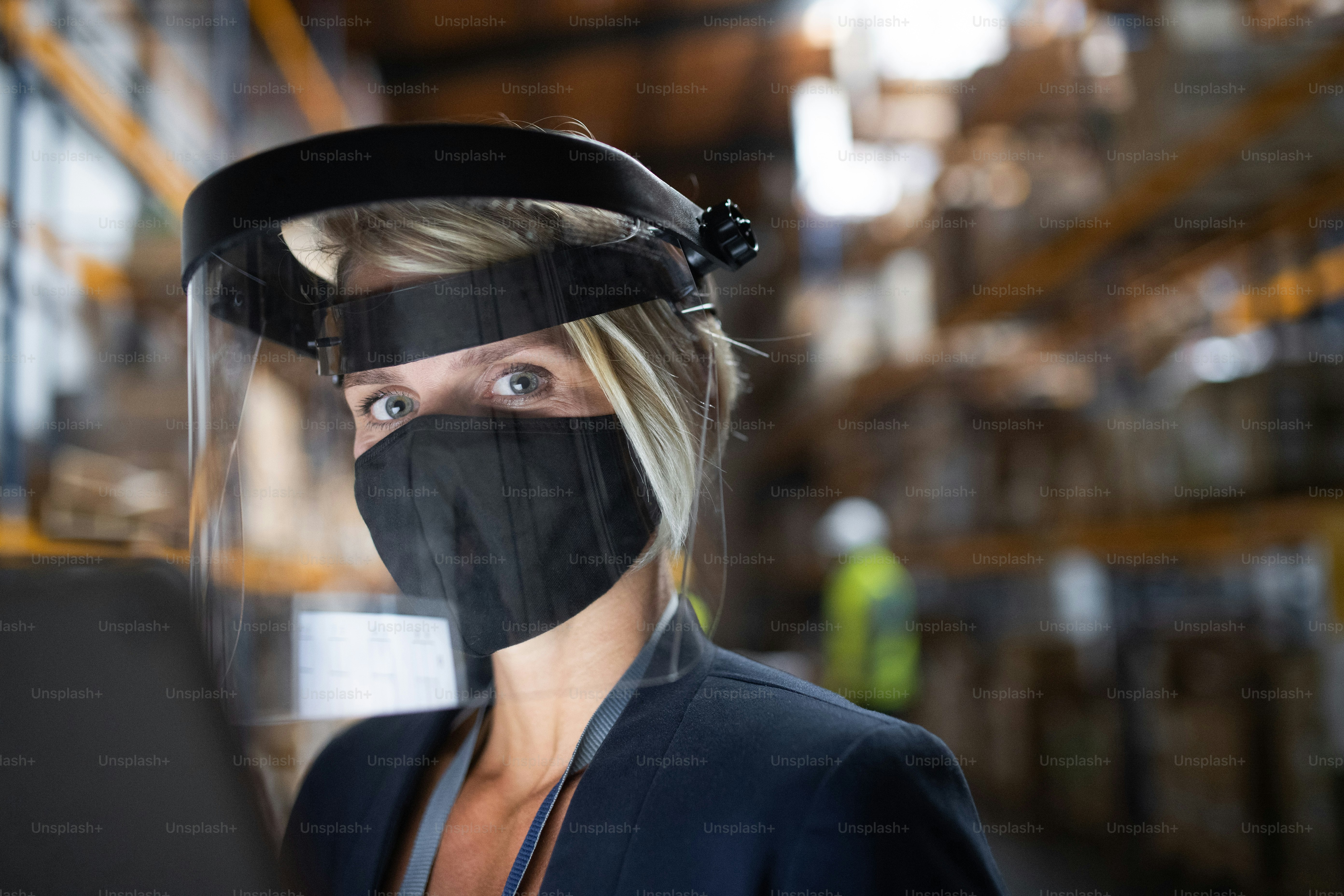 Manager with protective shield standing and looking at camera indoors ...