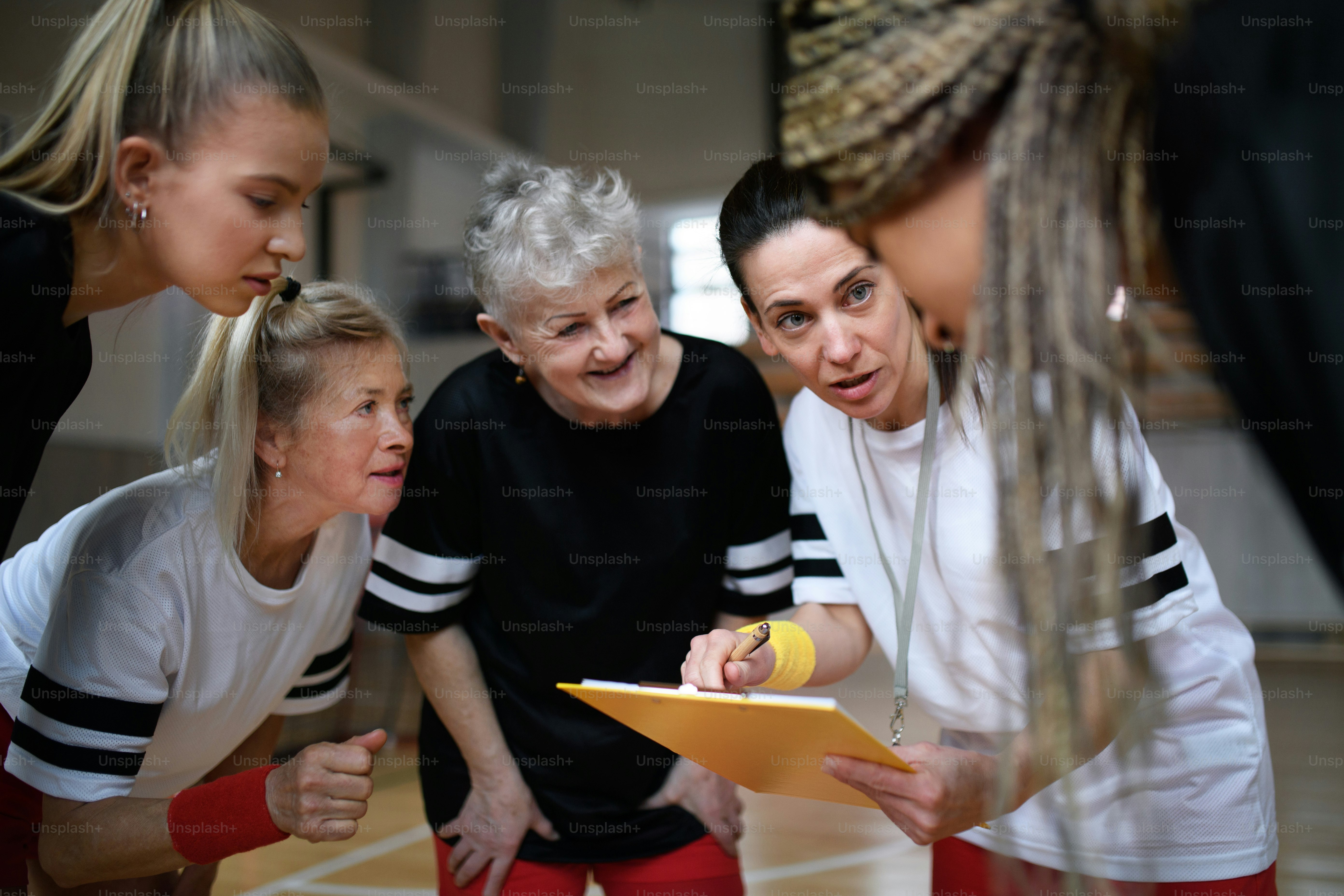 A female sport coach with clipboard discussing tactics with young and ...
