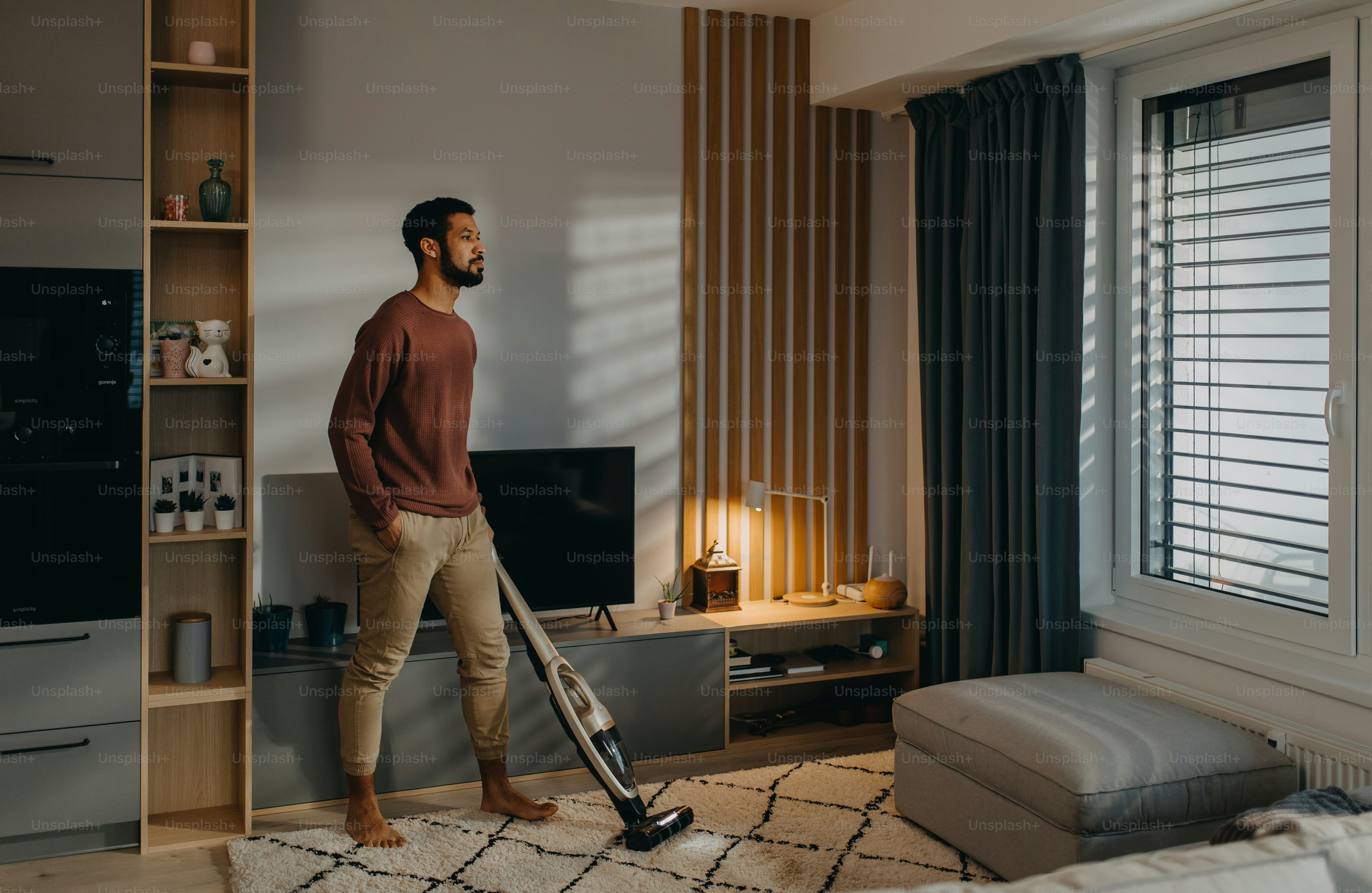 A lowsection of man hoovering carpet with vacuum cleaner in living room ...
