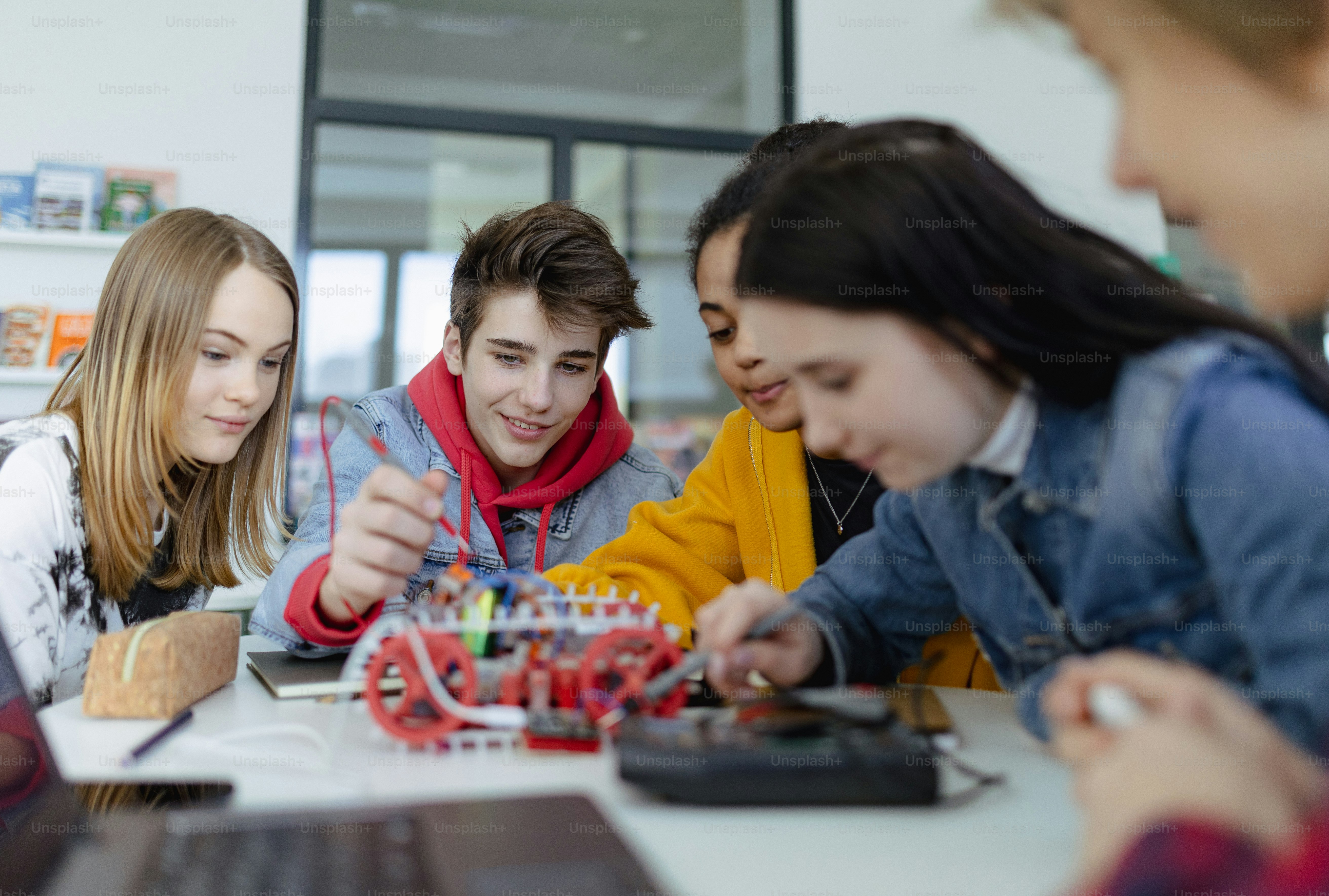 A group of students building and programming electric toys and robots at robotics classroom ...