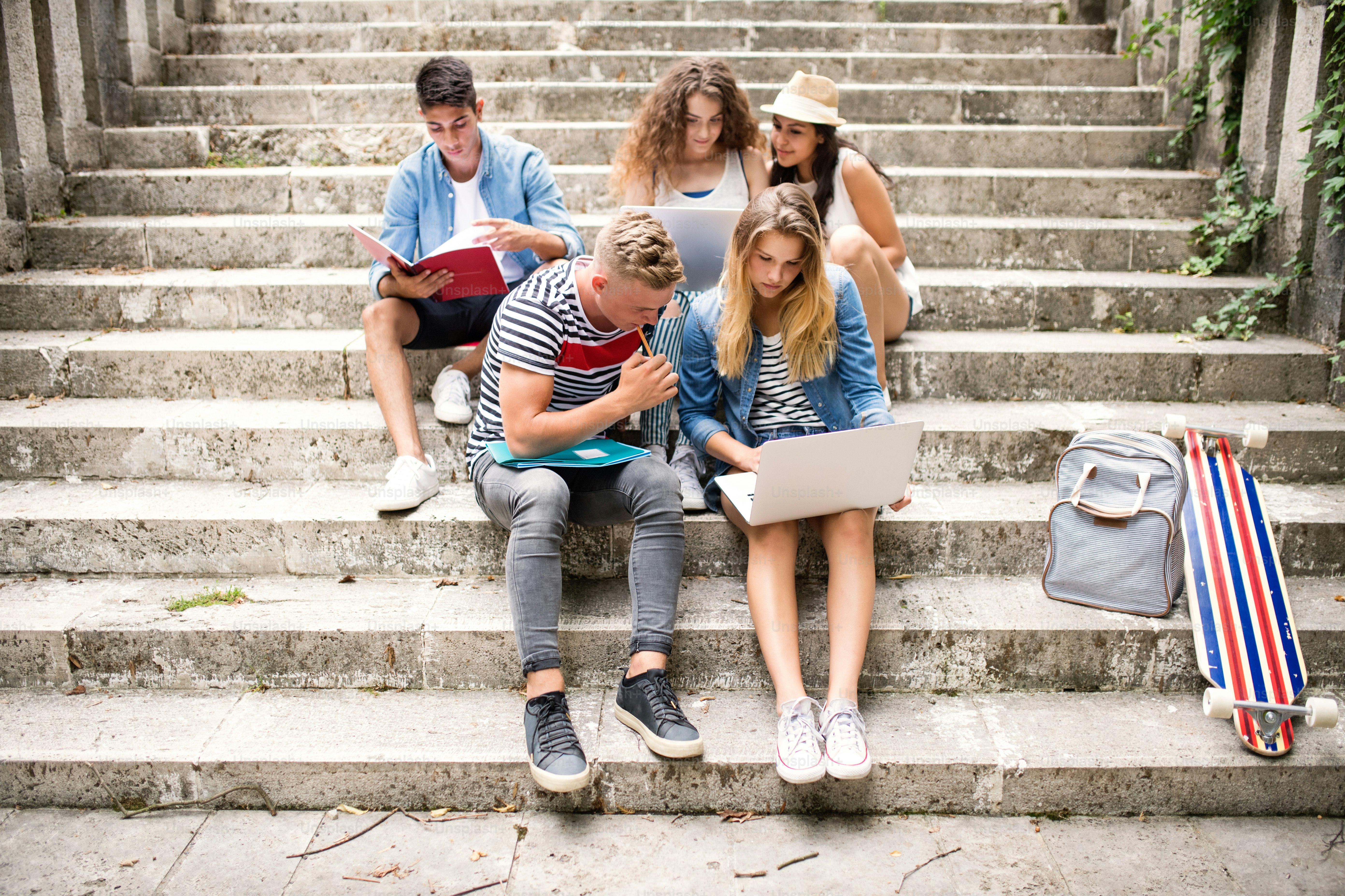 Group of attractive teenage students sitting on stone steps in front of ...
