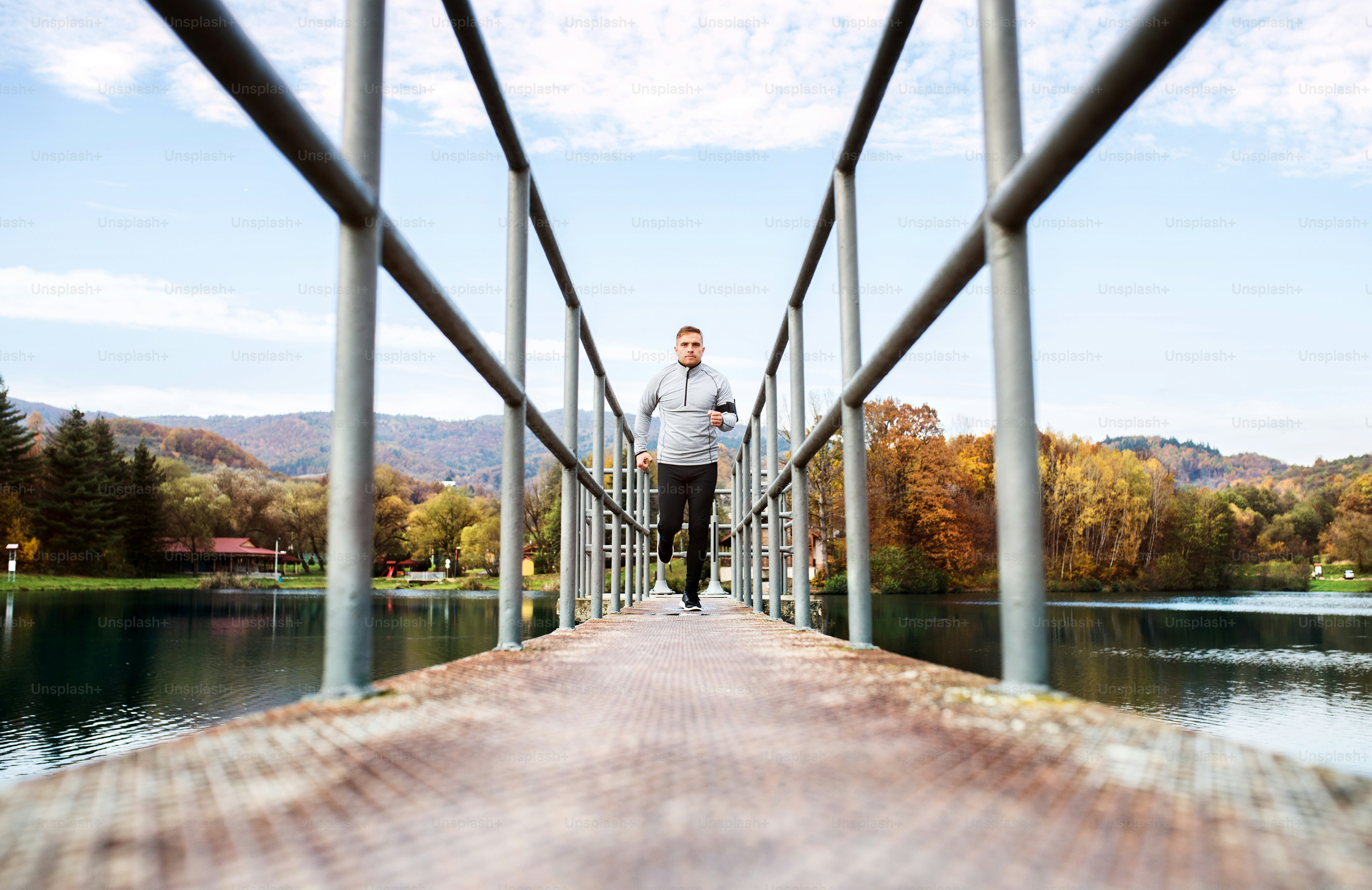 Young athlete with smartphone in gray jacket running outside. Trail ...