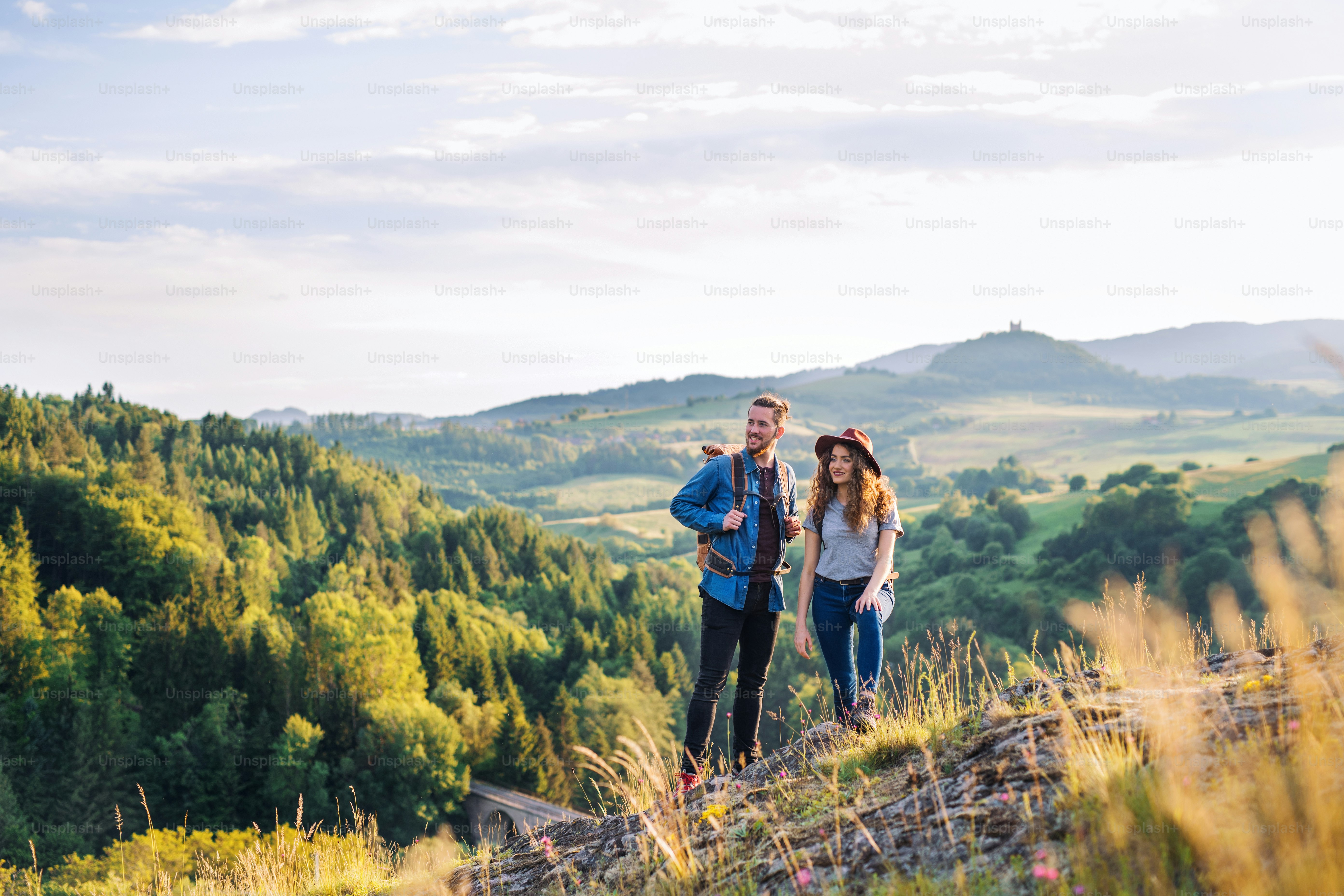 A young tourist couple travellers with backpacks hiking in nature ...