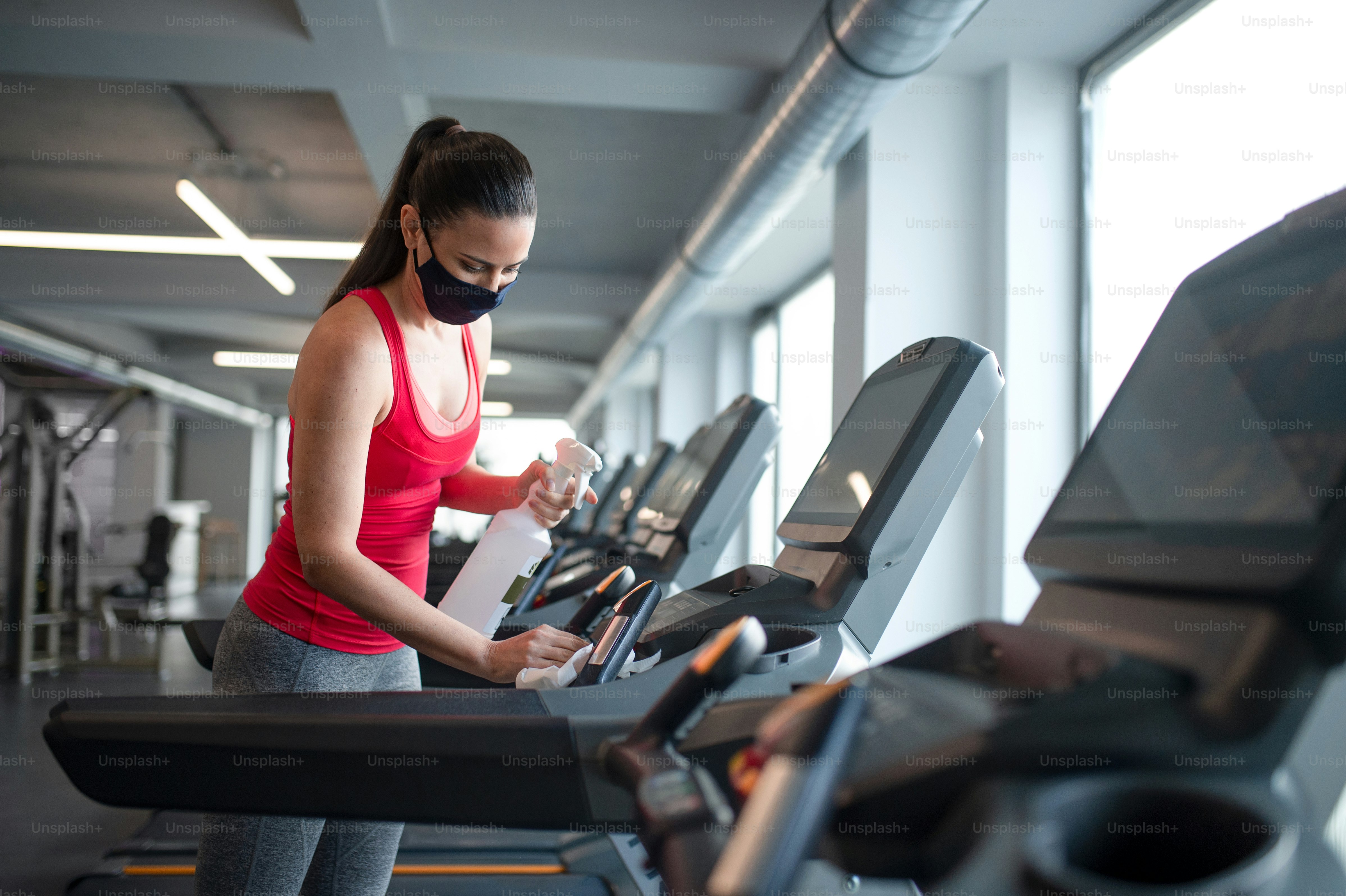 Fitness woman instructor with face mask disinfecting equipment in gym ...