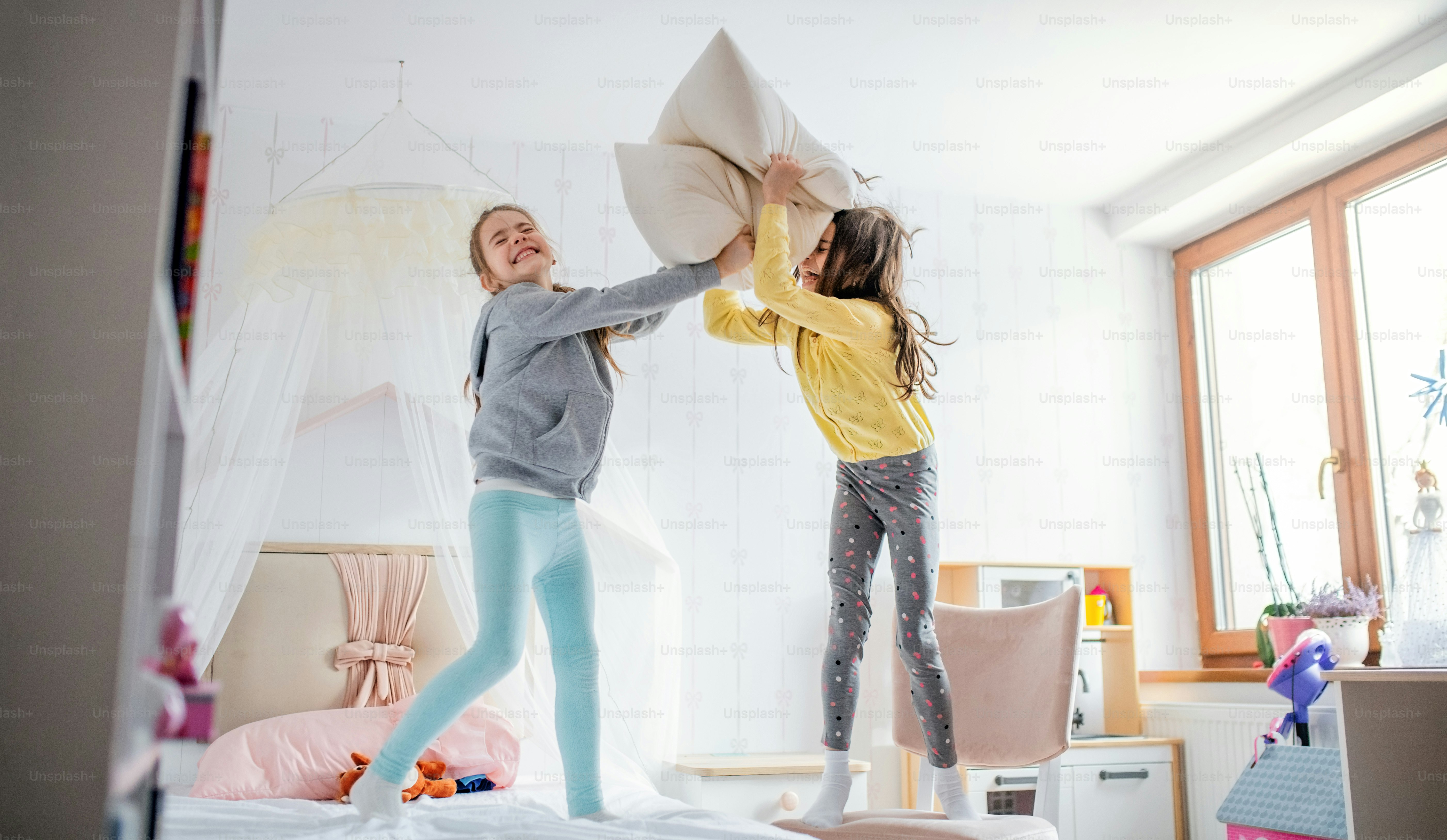 Two cheerful small girls sisters indoors at home, having fun under ...