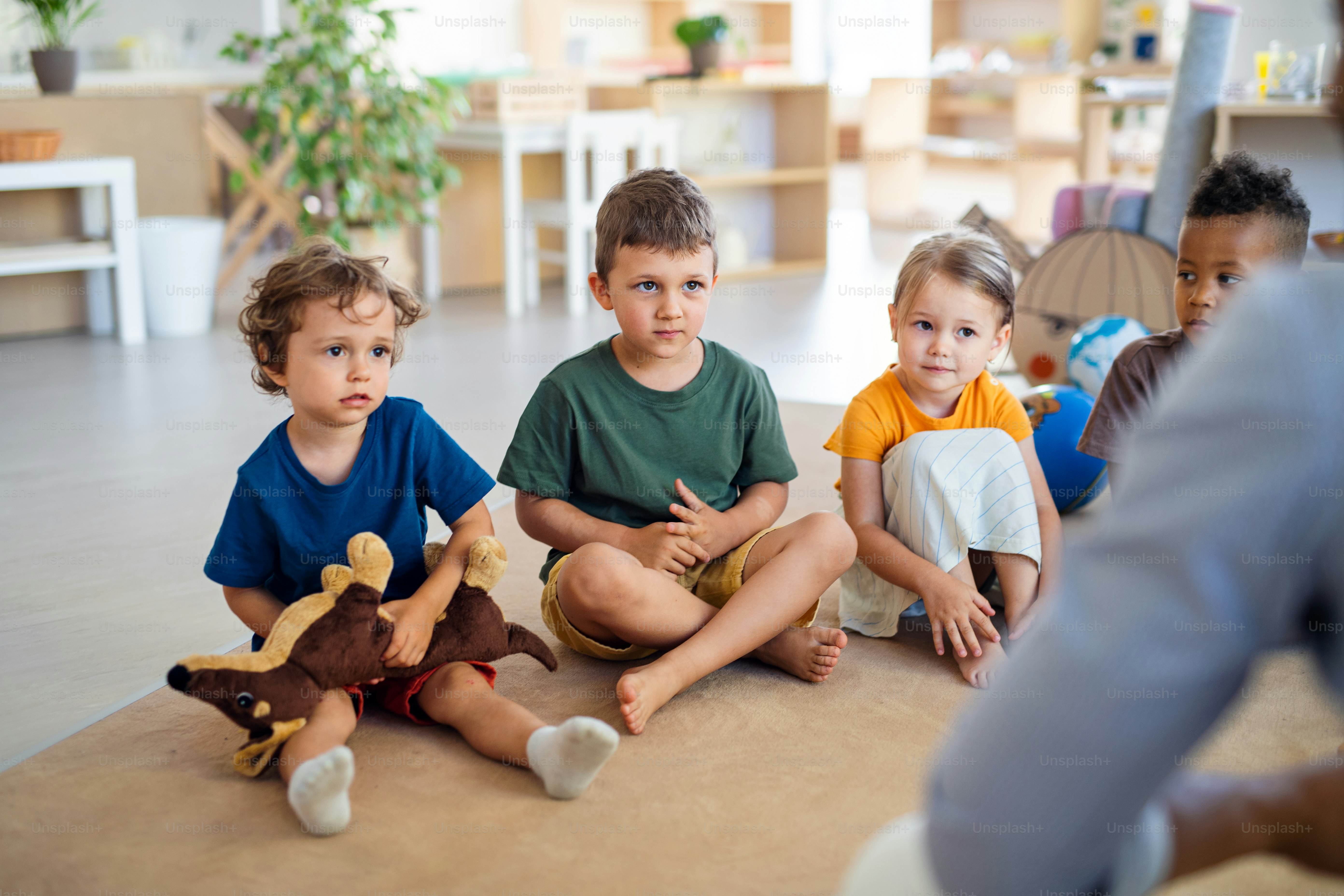 A group of small nursery school children sitting on floor indoors in ...