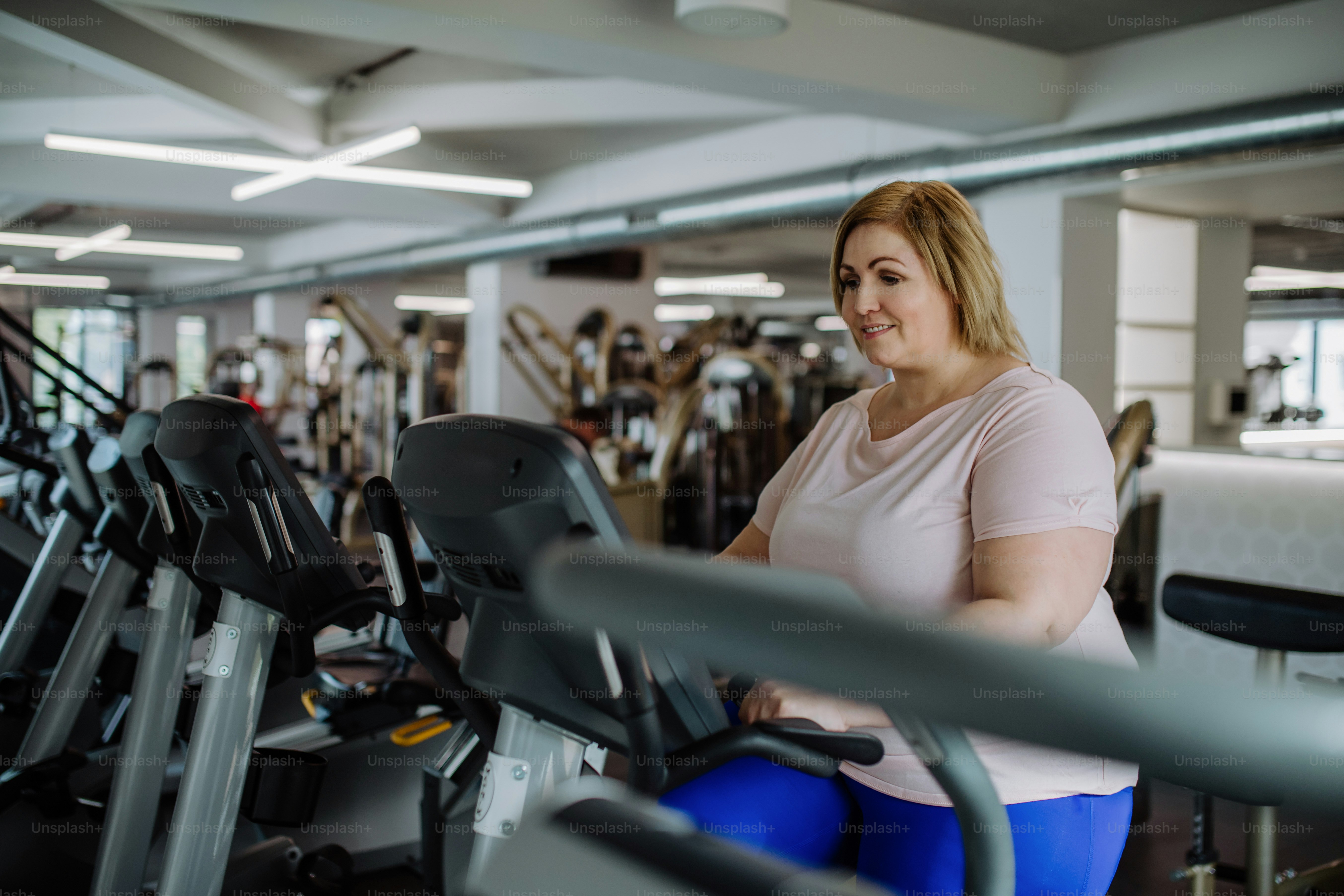 A happy mid adult overweight woman exercising on stepper indoors in gym ...
