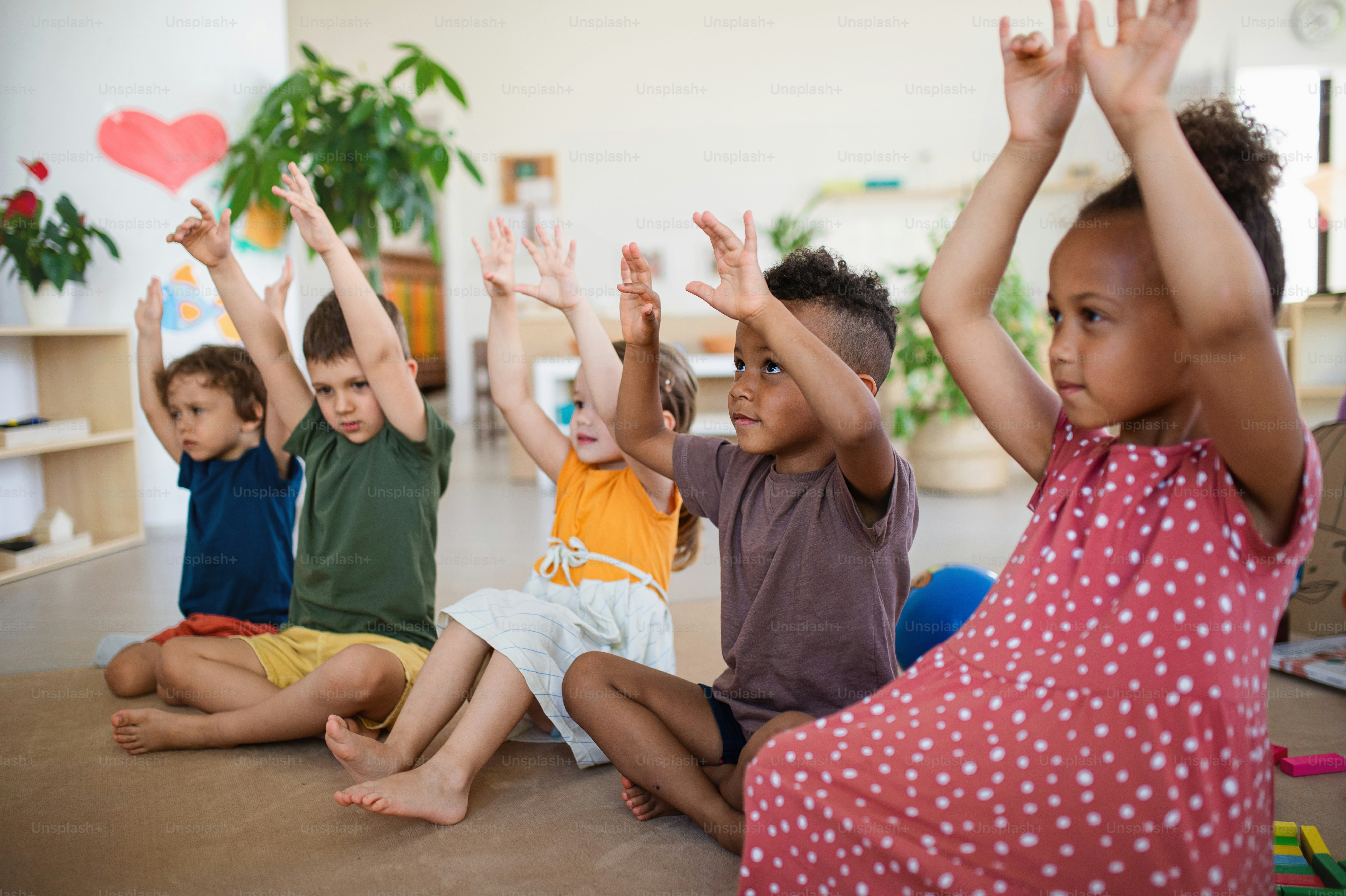 A group of small nursery school children sitting on floor indoors in ...