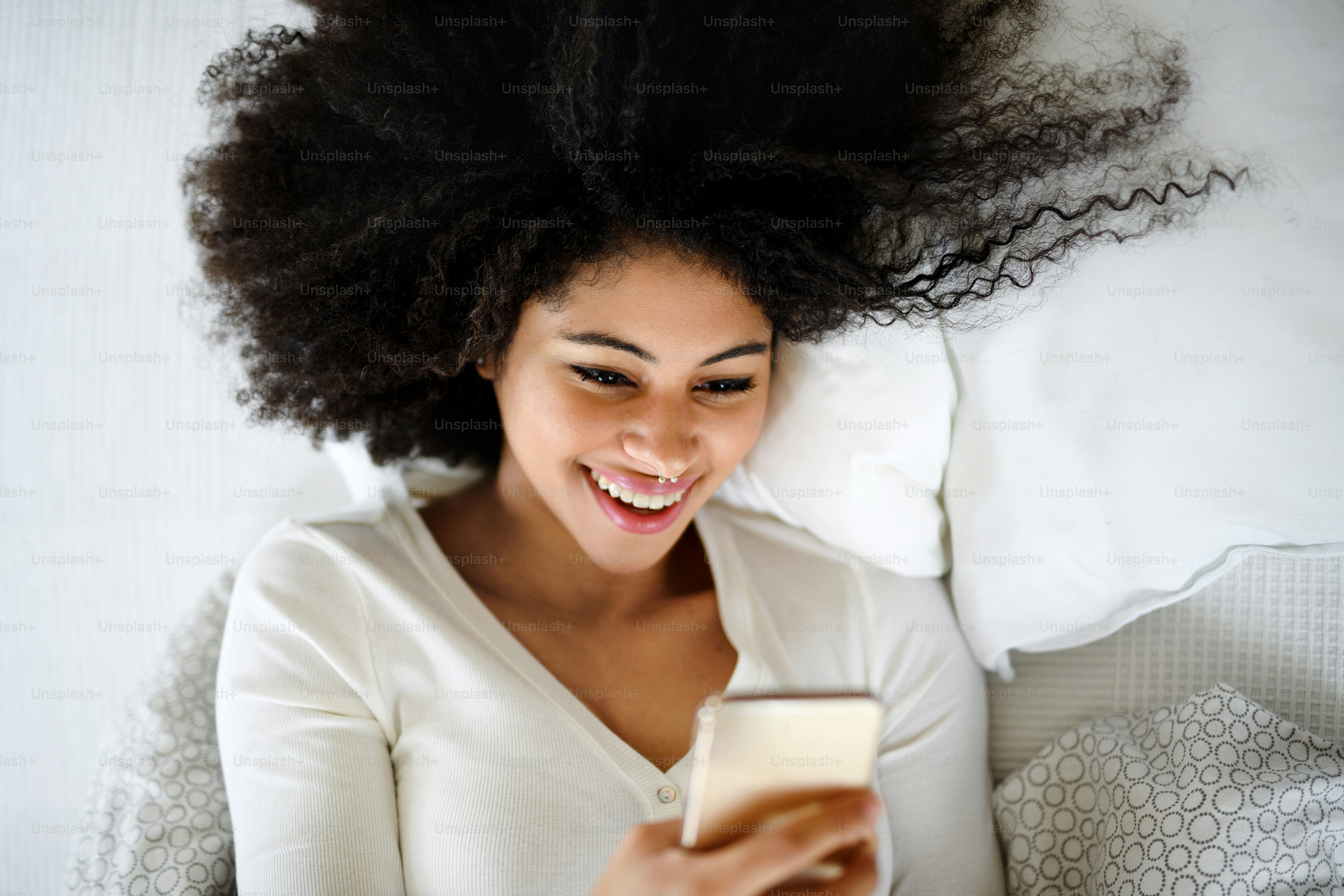Top view portrait of happy young woman indoors on bed, using smartphone ...