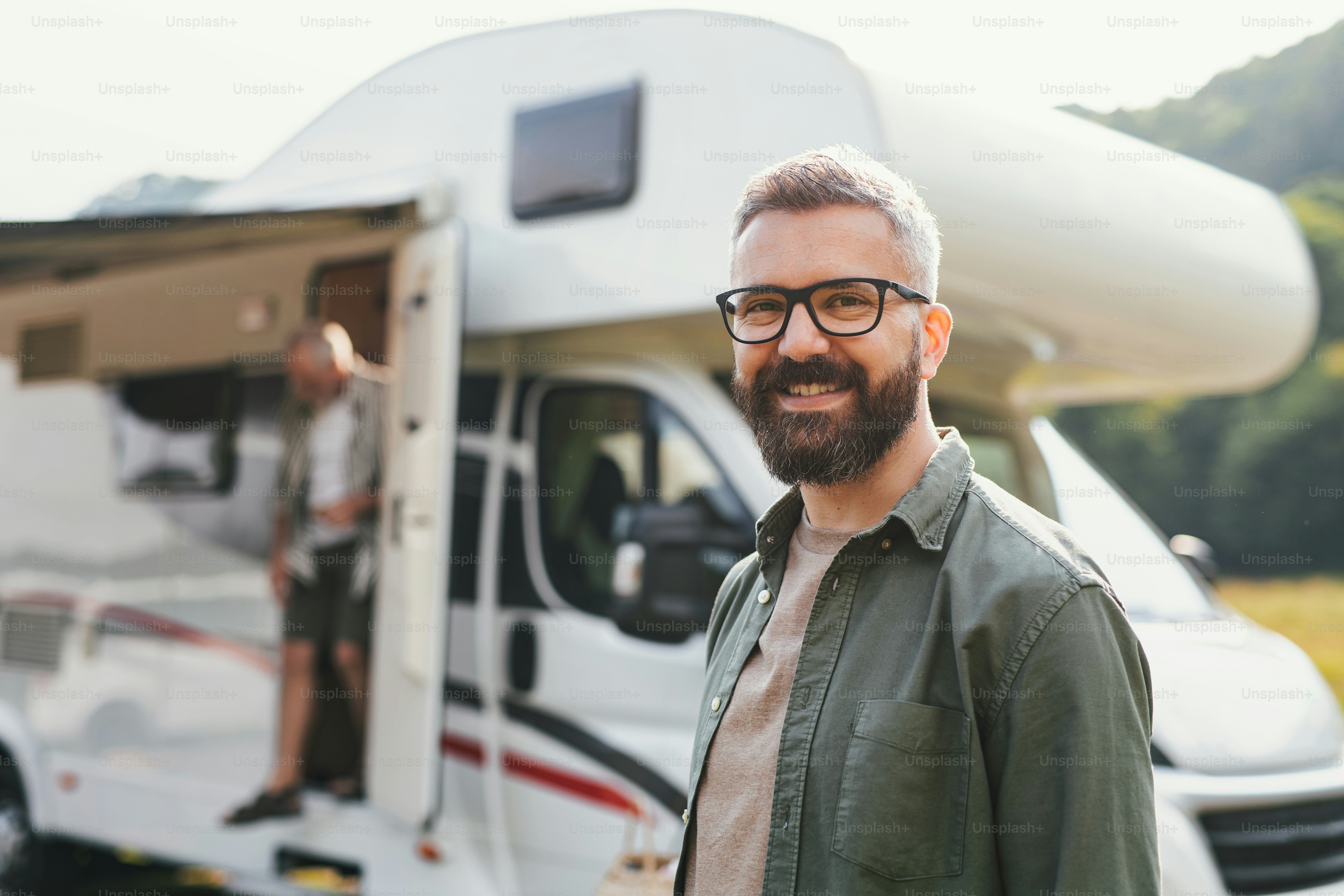 A portrait of happy man standing by car outdoors in campsite, looking ...