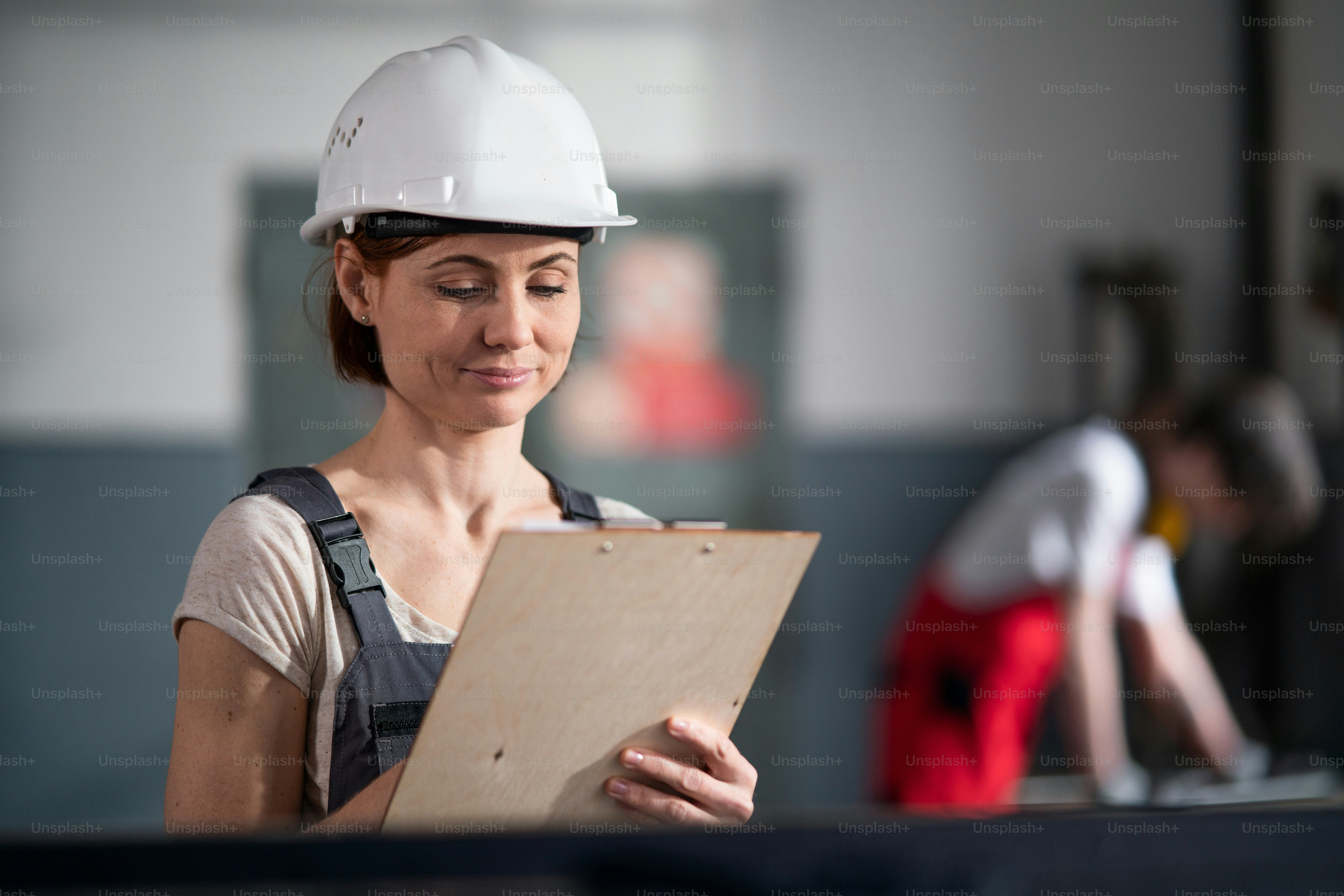 A low-angle view of worker with helmet and clipboard indoors in factory ...