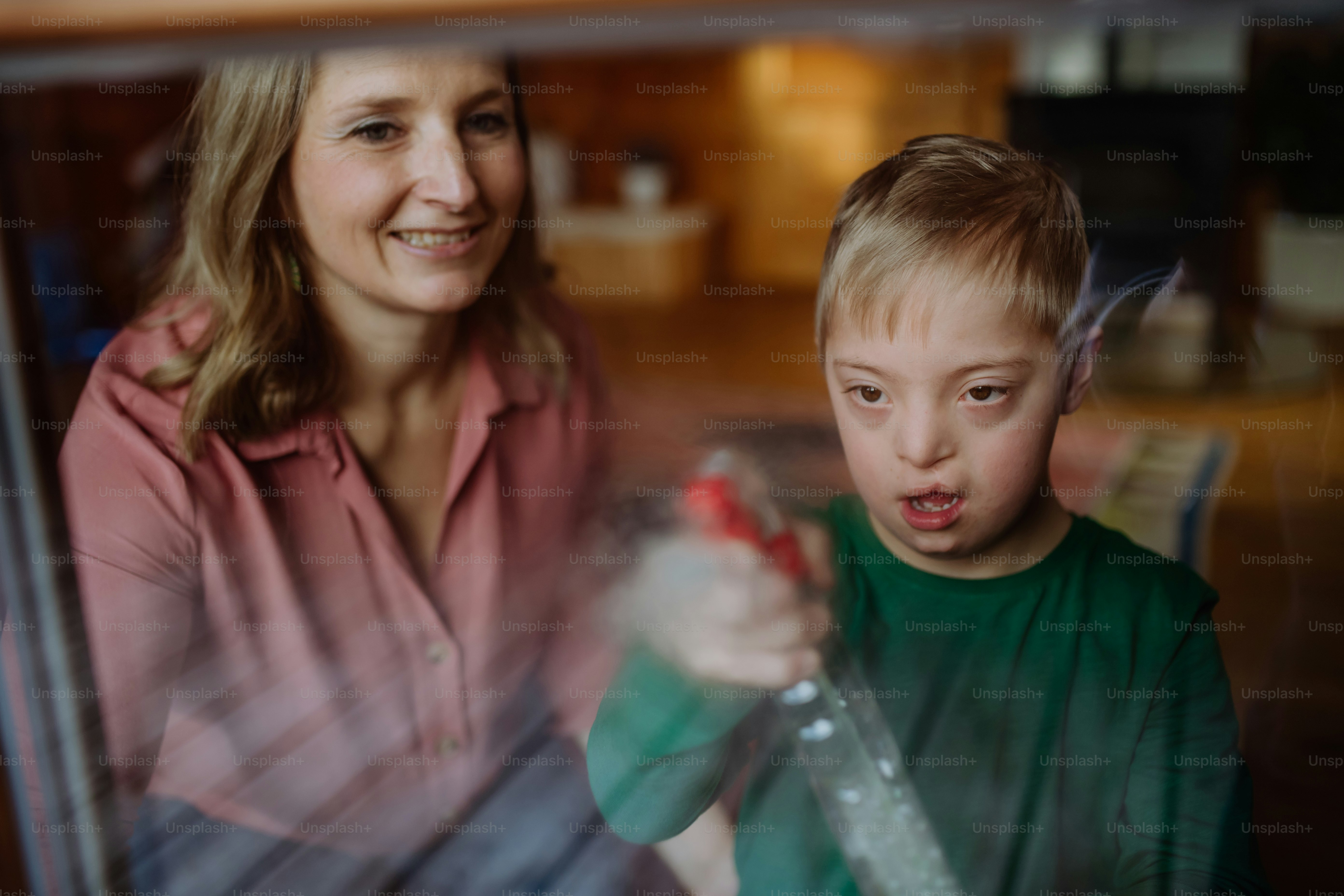 A boy with Down syndrome with his mother cleaning window at home. photo ...