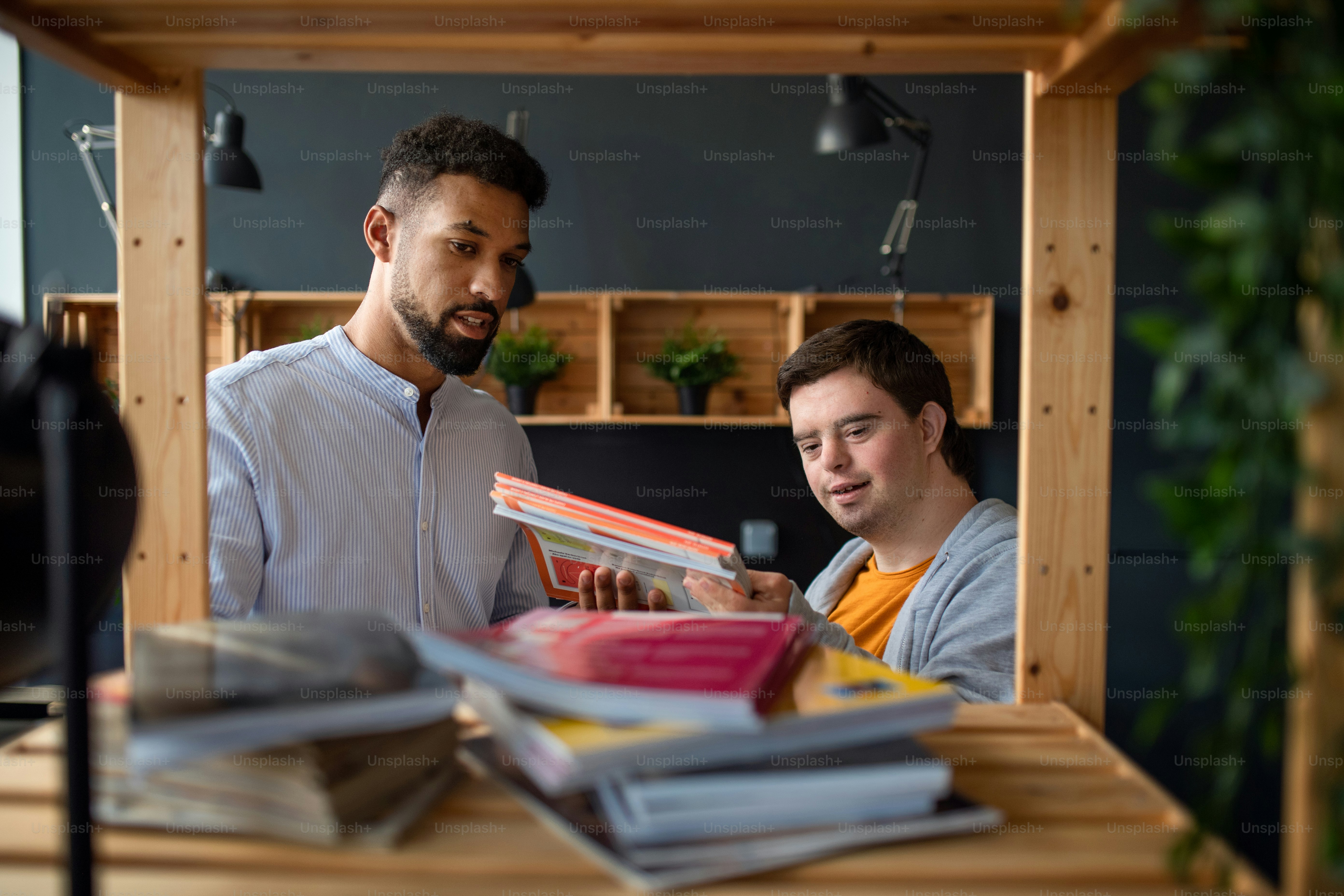 A young happy man with Down syndrome and his tutor indoors at staffroom ...