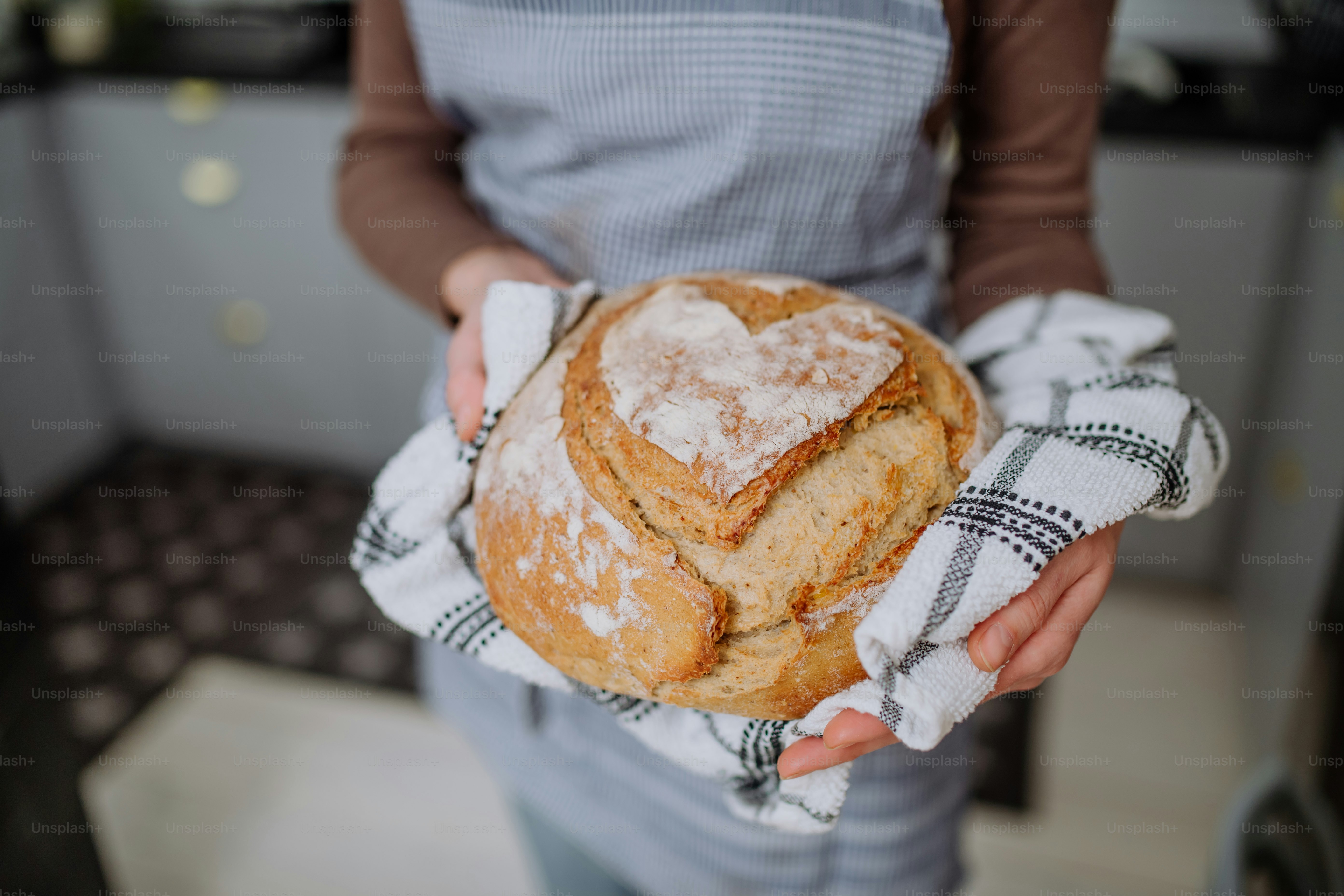 A close-up of woman holding homemade sourdough bread, cooking at home ...