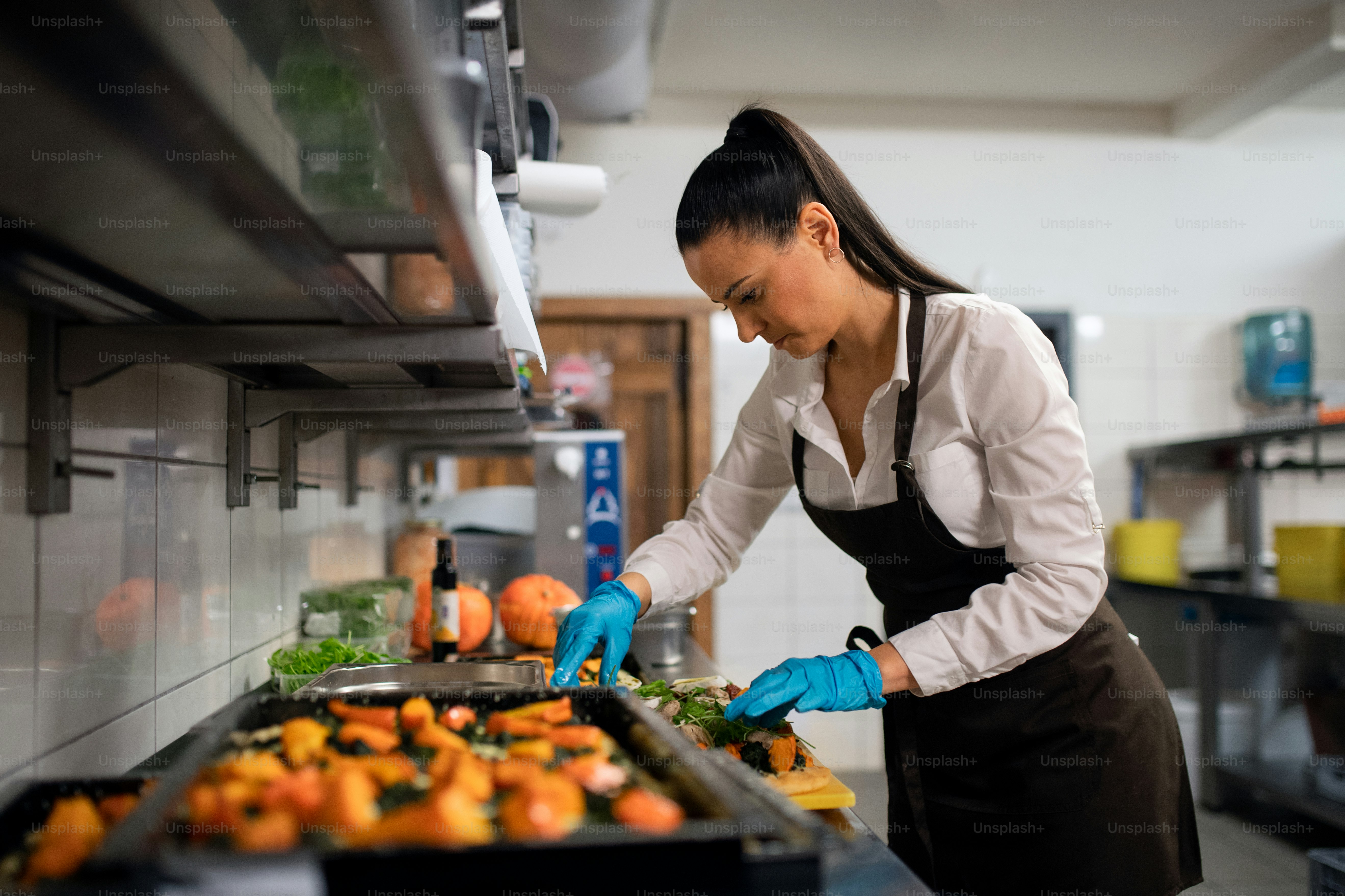 A professional chef working on her dishes indoors in restaurant kitchen ...