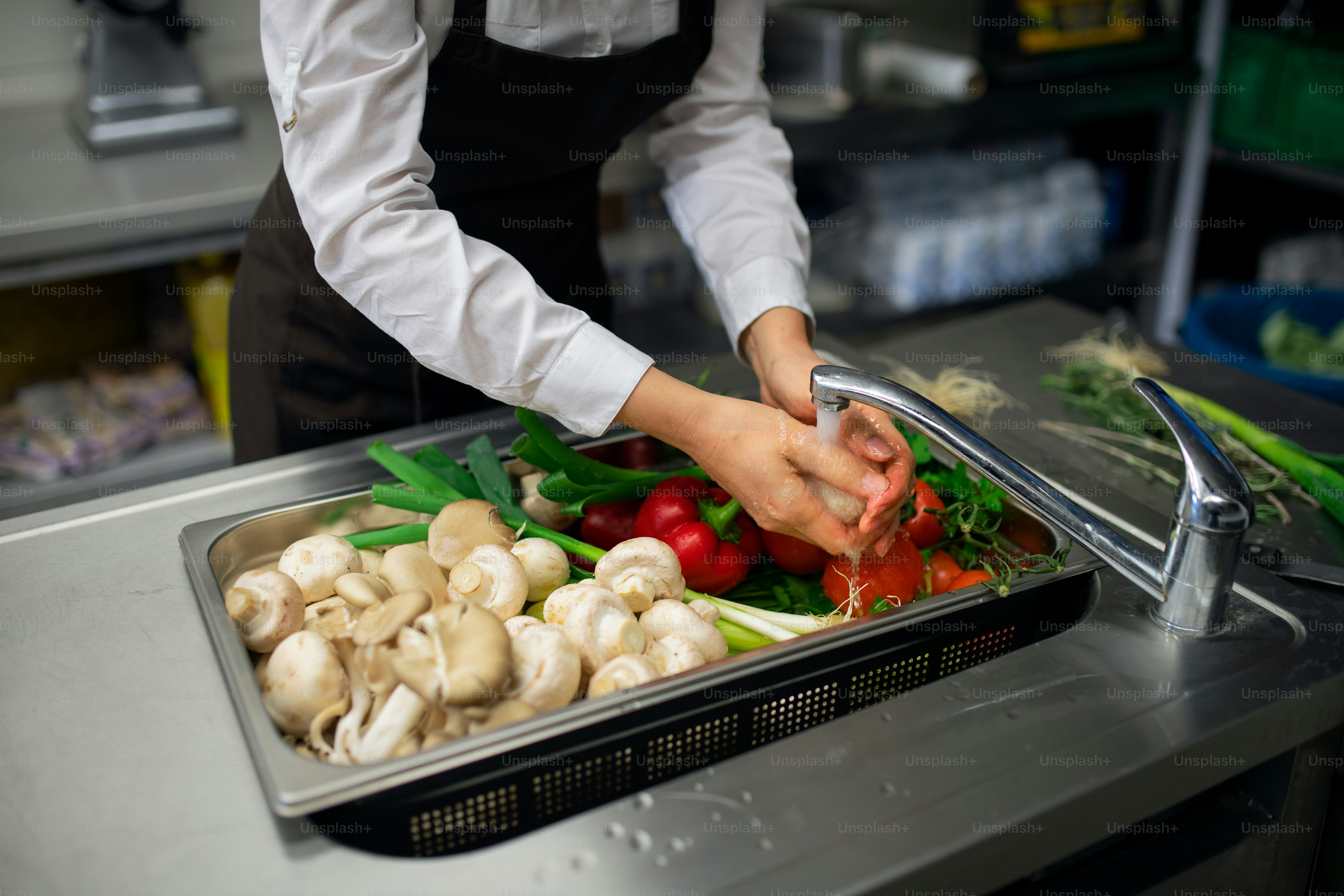 A close-up of cook washing vegetables in sink in commercial kitchen ...
