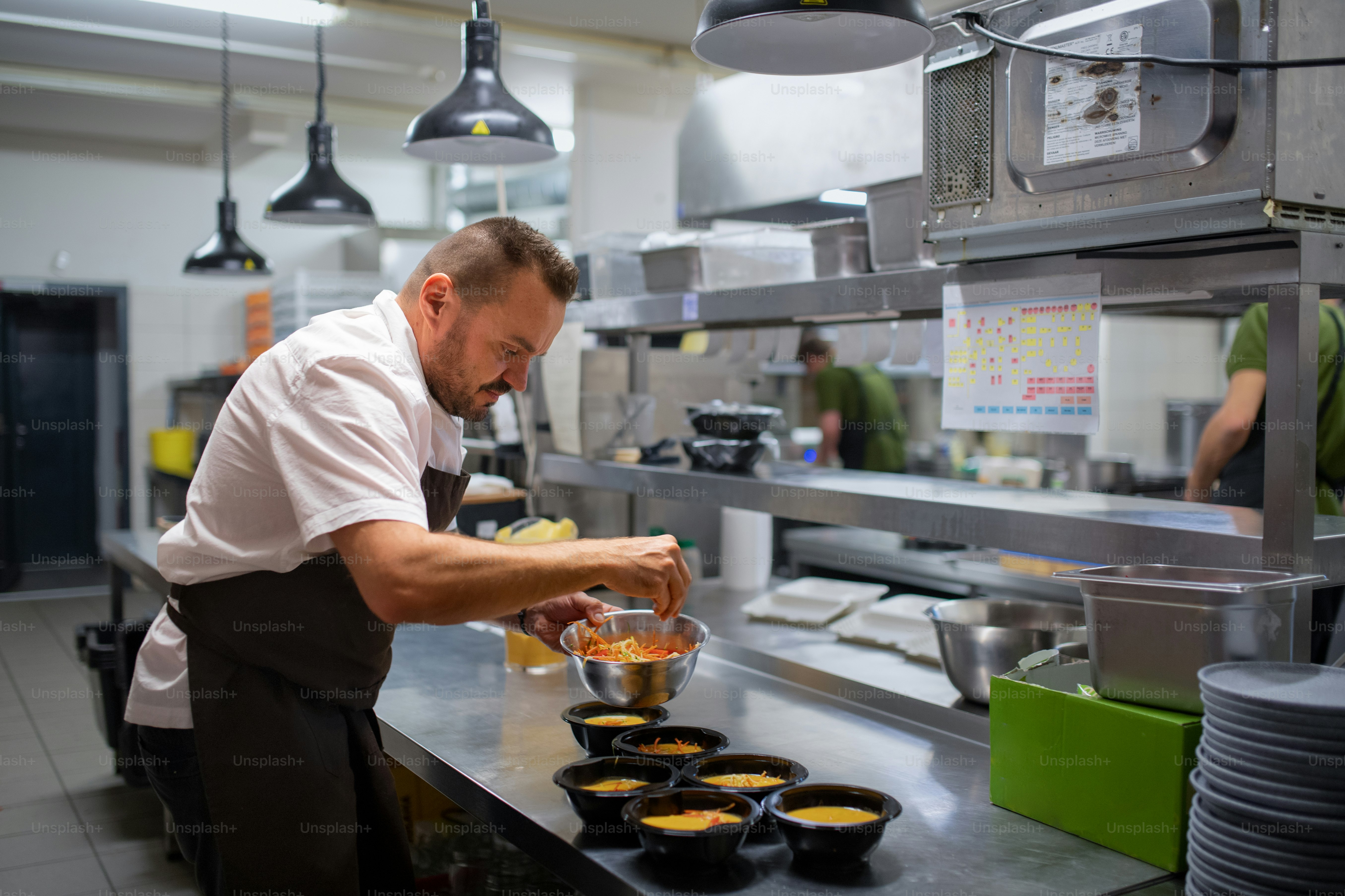 A chef decorating soups in takeaway bowls indoors in restaurant kitchen ...