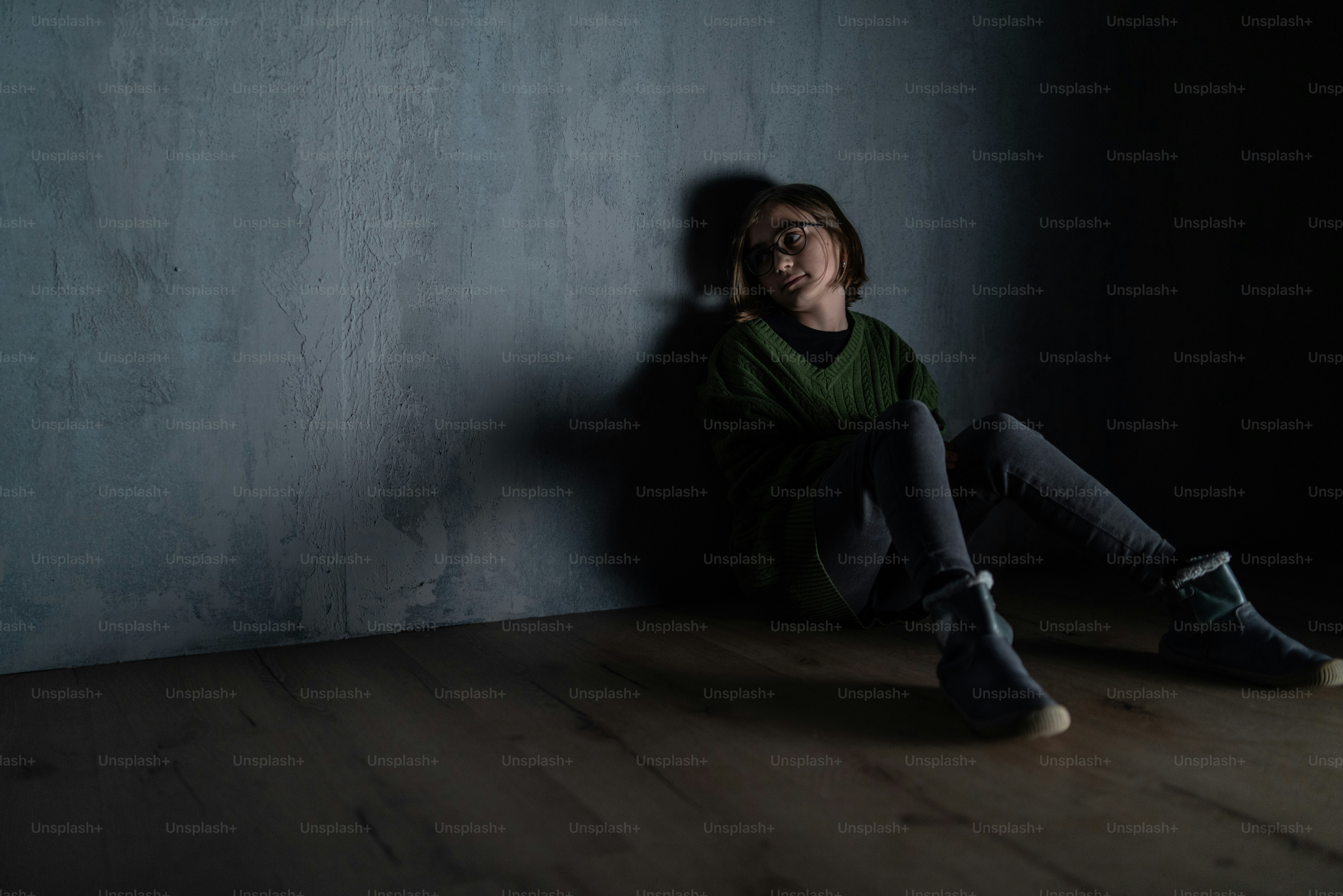 A sad little girl, alone in darkness, sitting and and covering face ...