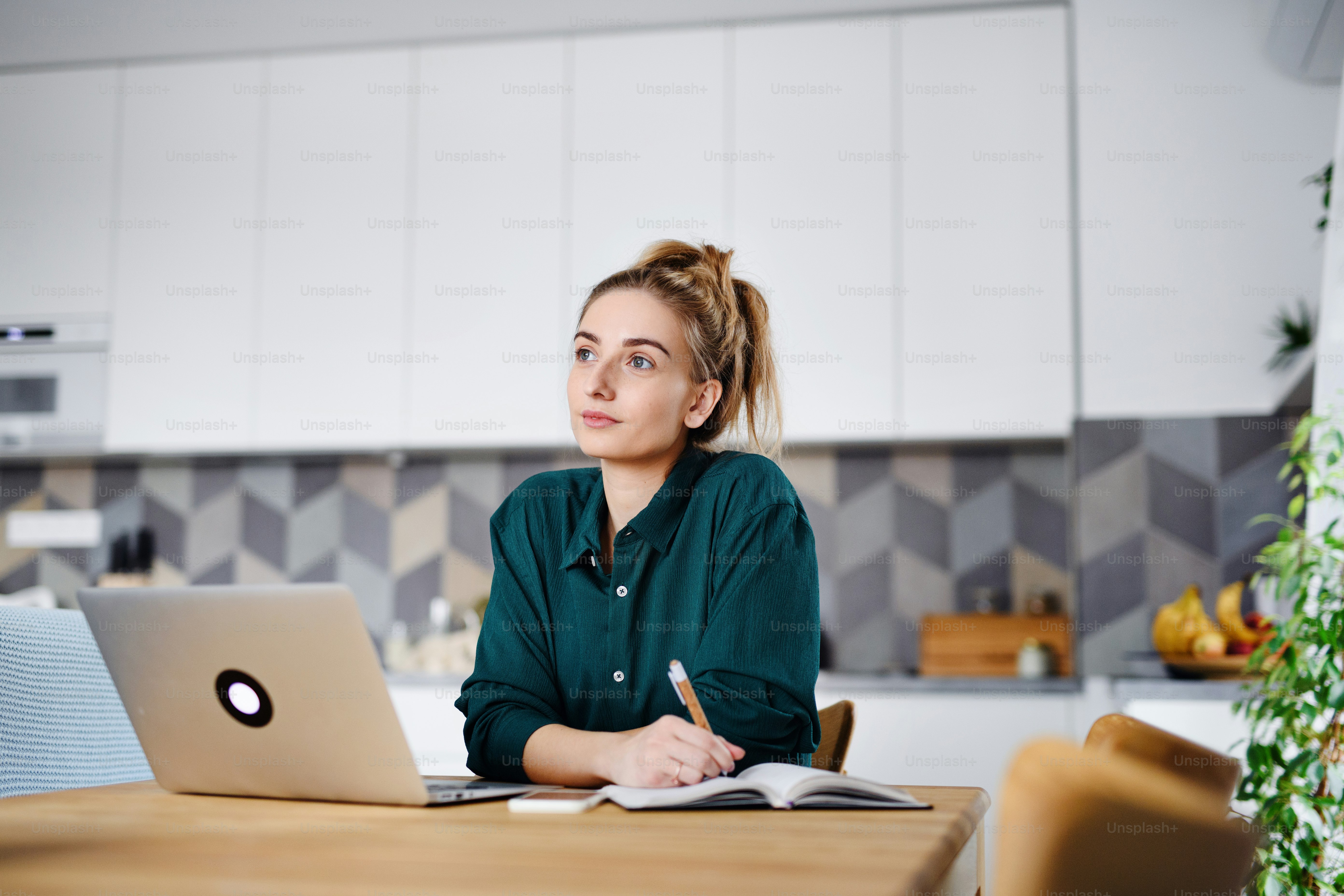 A young woman student with laptop writing notes at home, home office ...