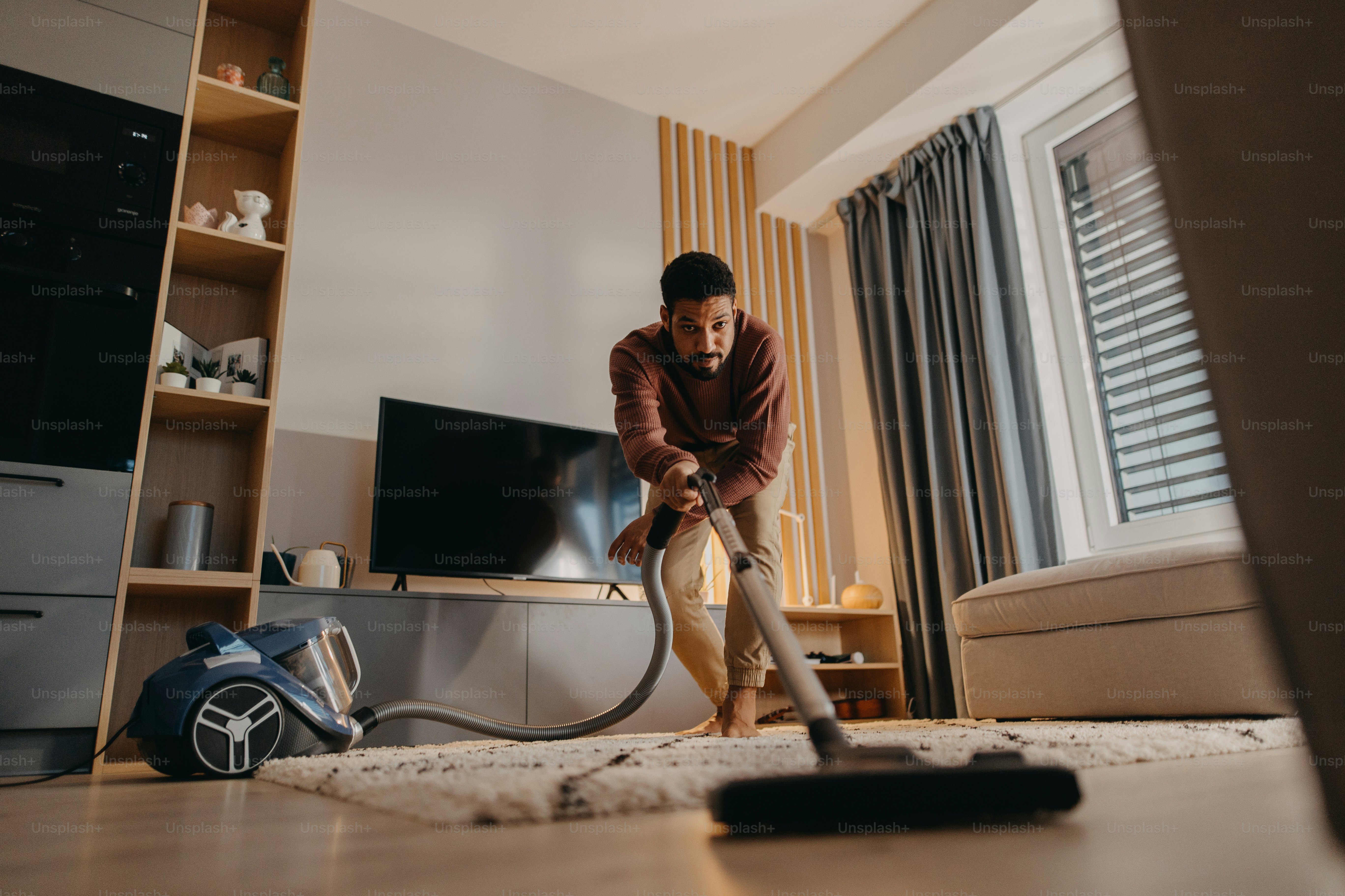 A young man hoovering carpet with vacuum cleaner in living room photo ...