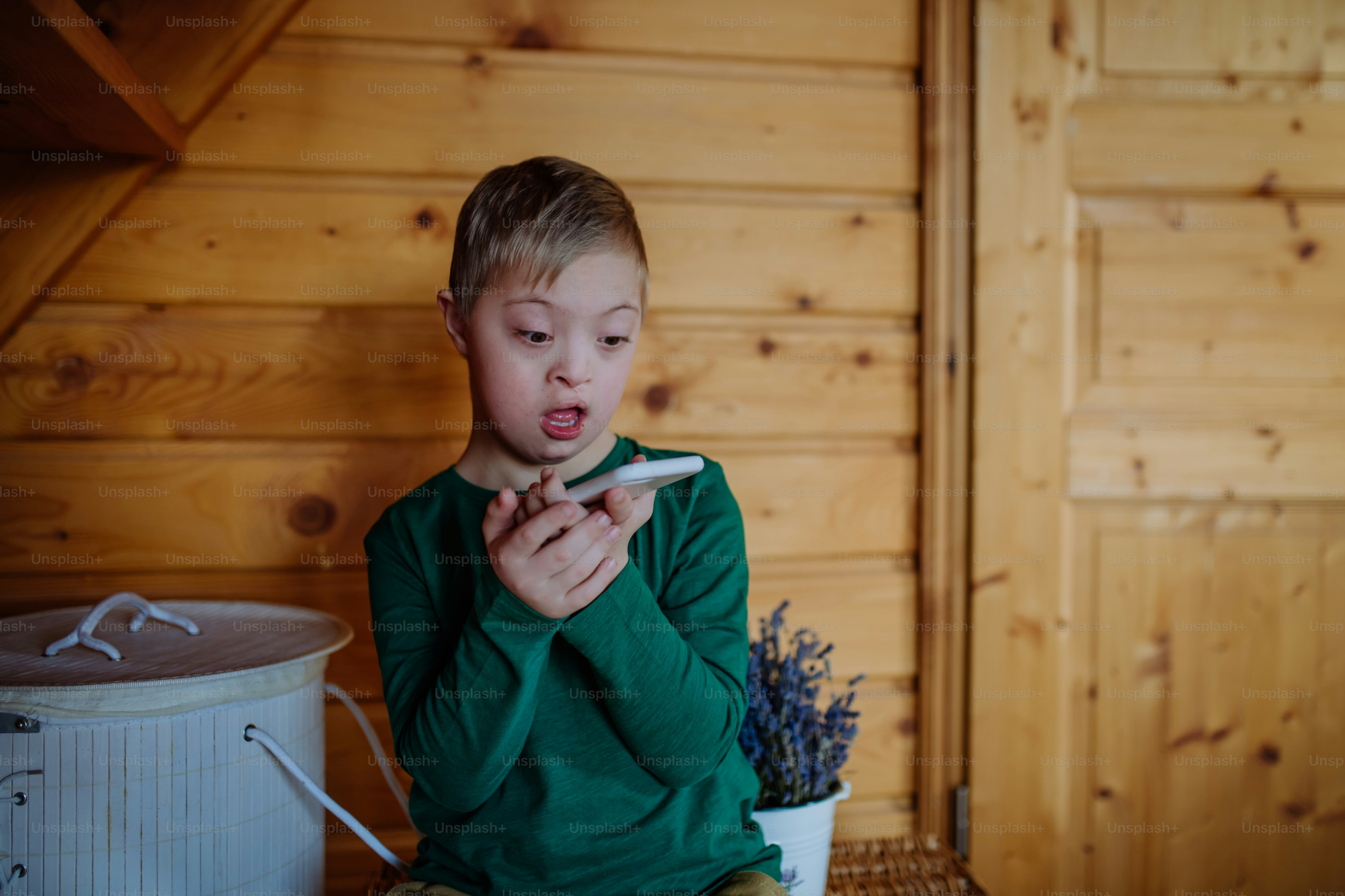 A sad little boy with Down syndrome sitting on floor and looking ...